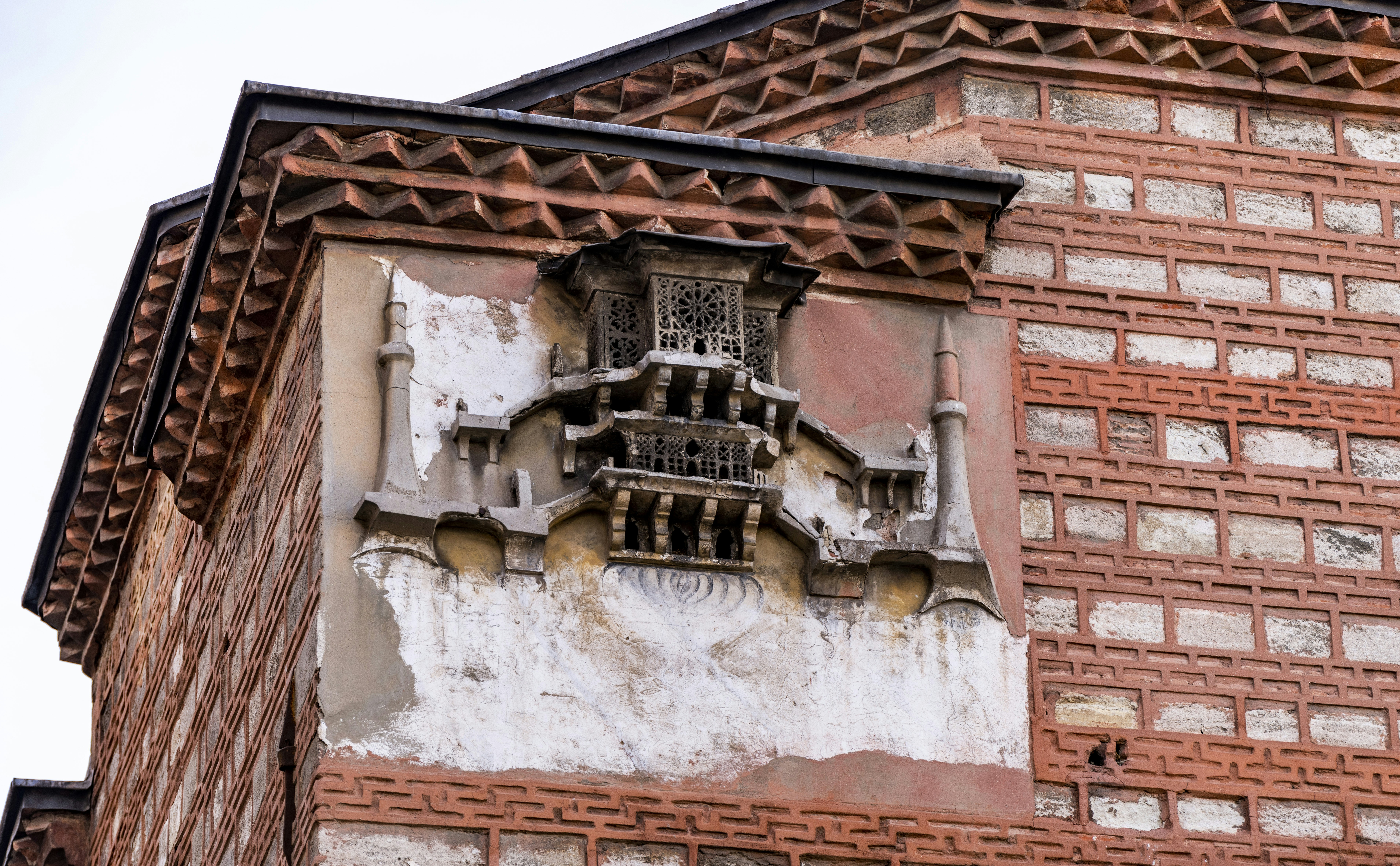 Ornate Balcony Pierced into a Weathered Red Brick Facade