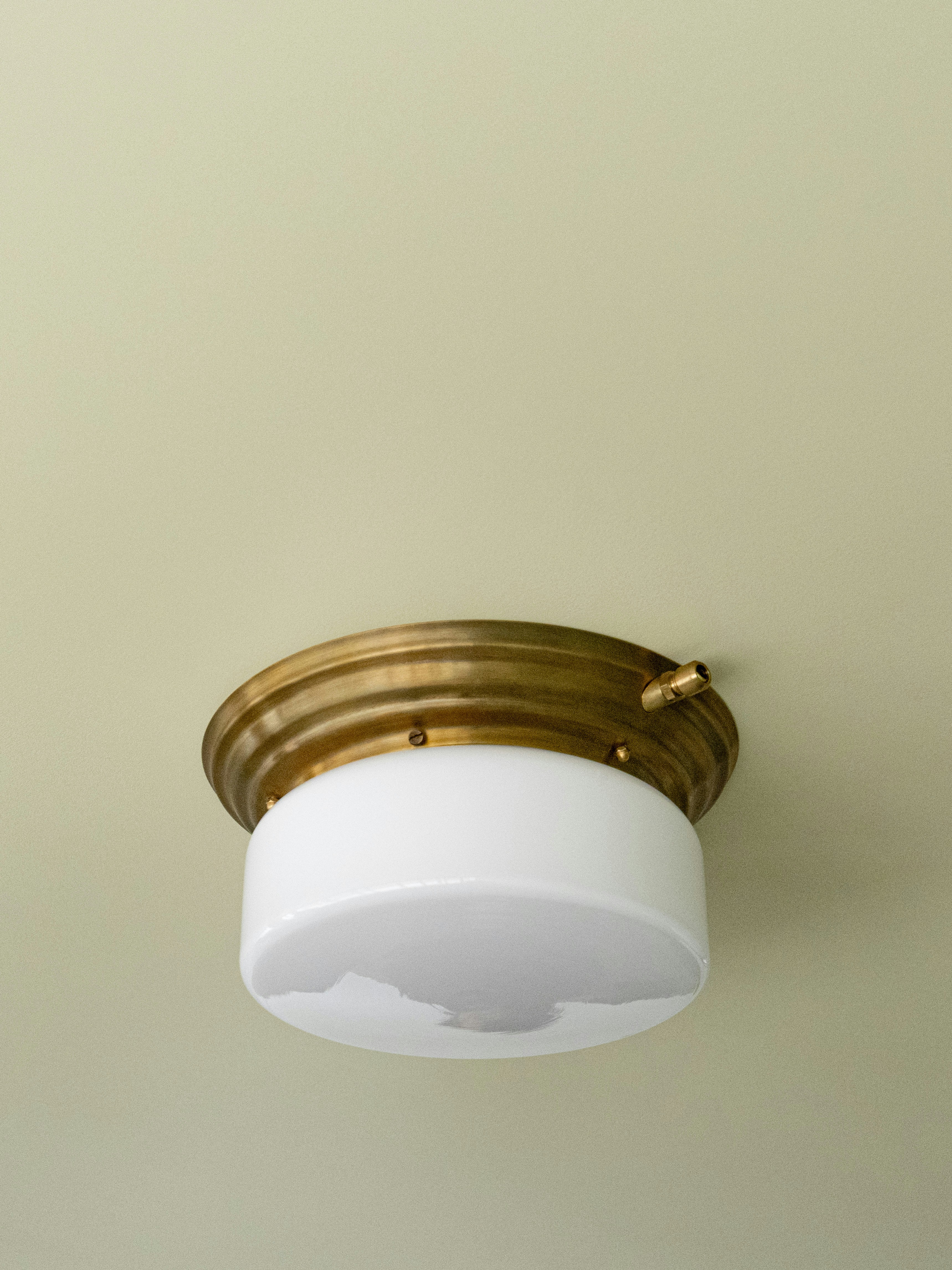 Close-up of a white circular ceiling light with a brass rim mounted on a pale olive-green ceiling.