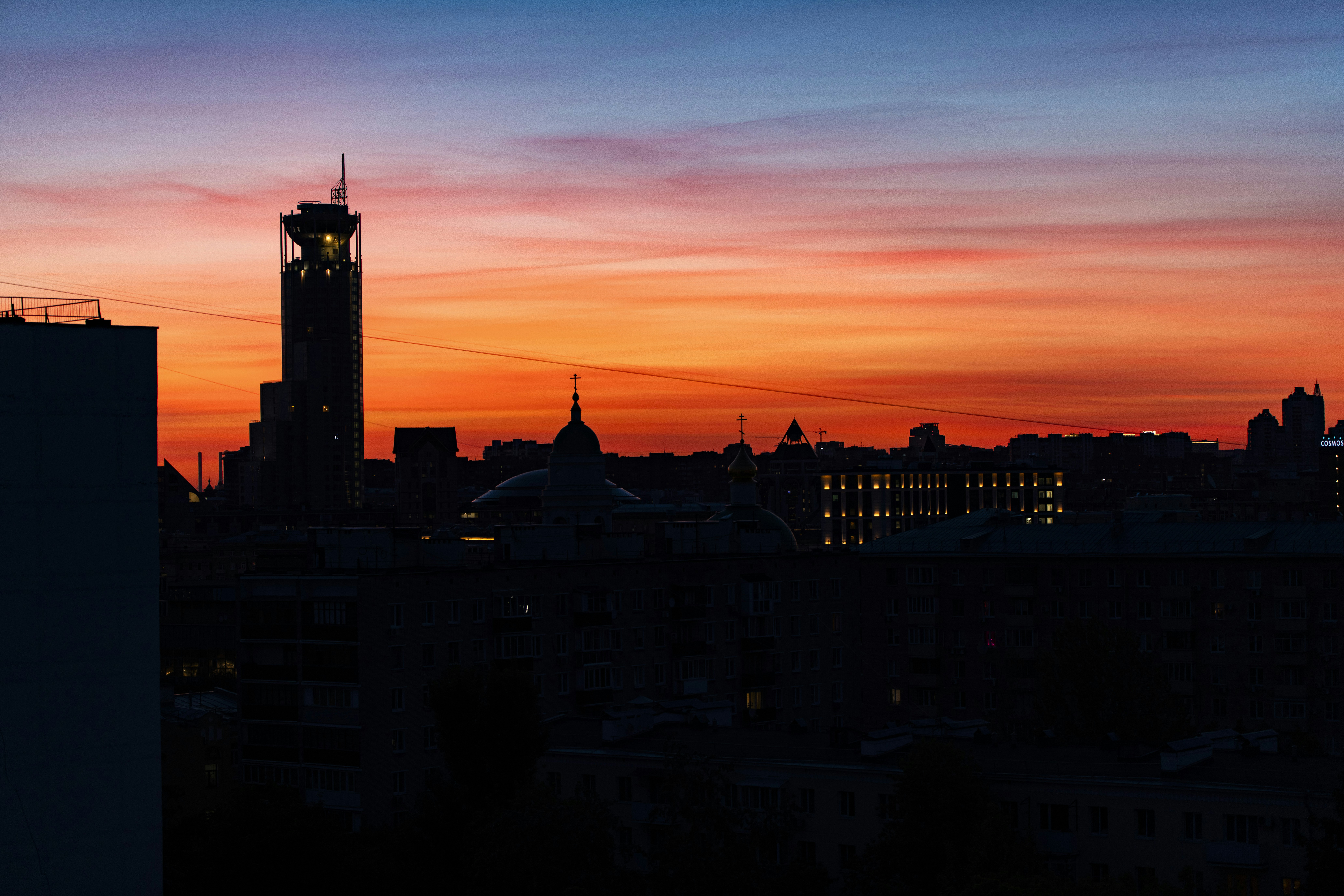 City skyline silhouetted against a vibrant sunset with deep orange and blue hues.