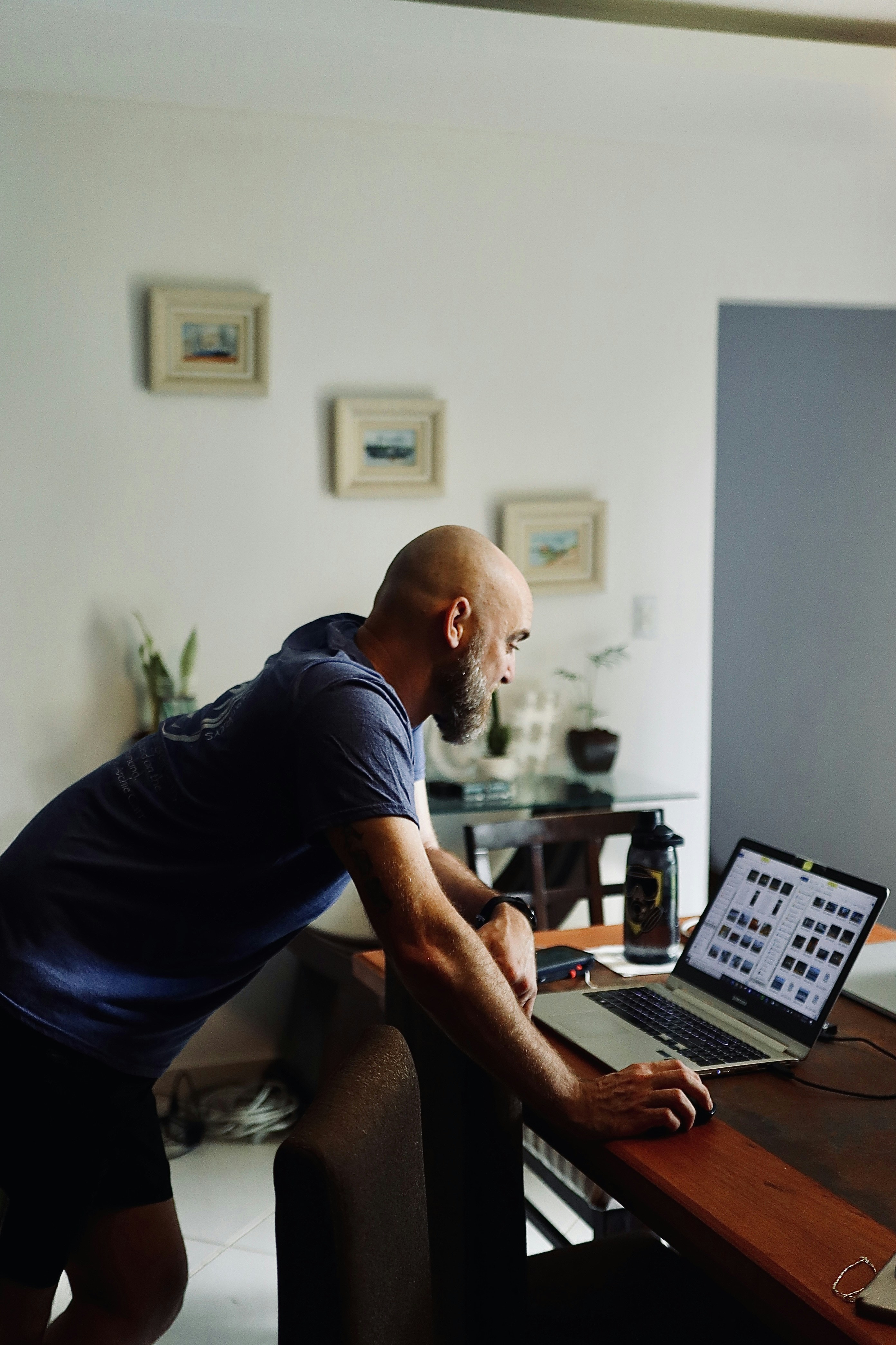 Person leaning over a wooden desk, intently viewing a laptop screen in a softly lit room.
