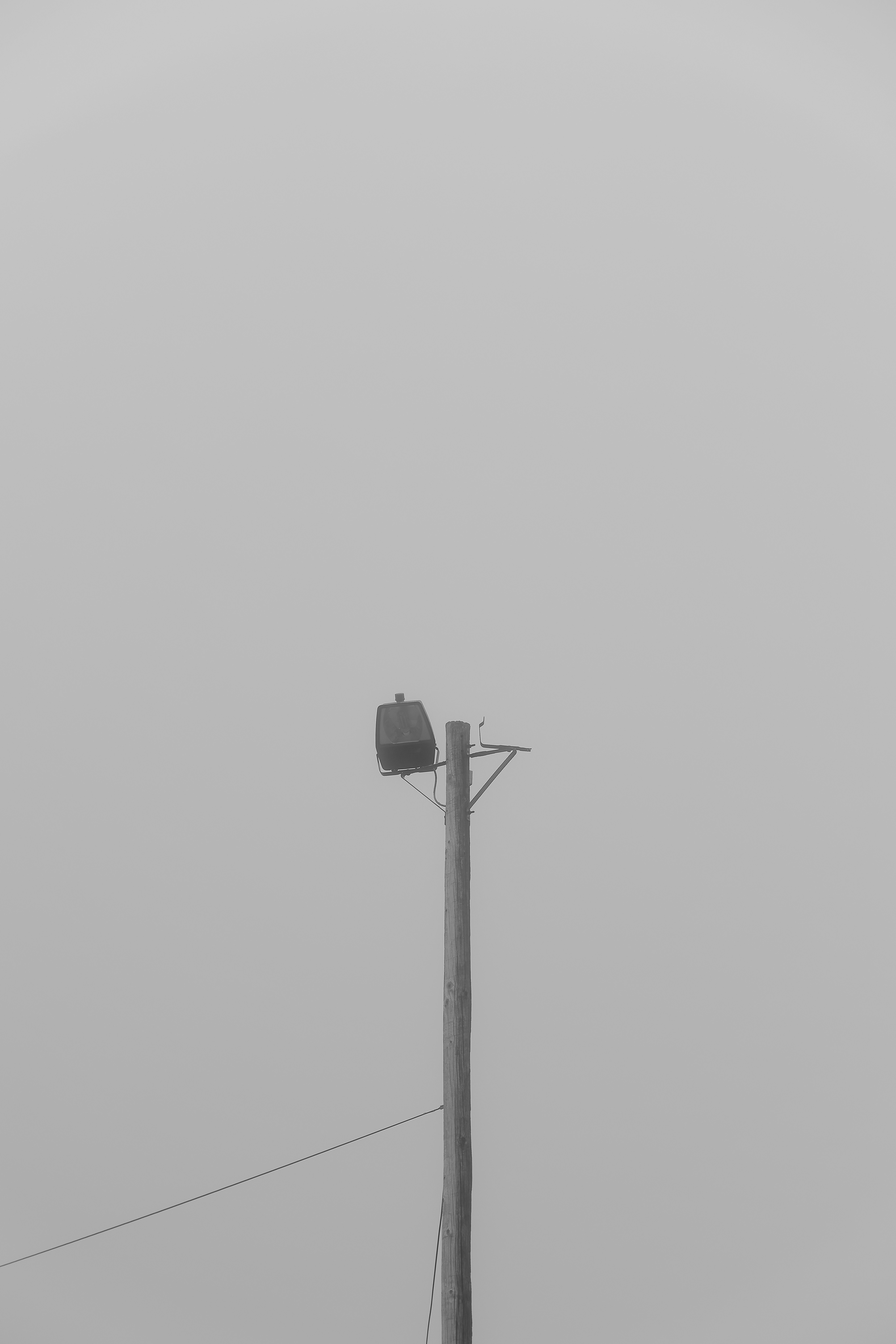 Lonely utility pole topped with a light against a foggy, gray sky.
