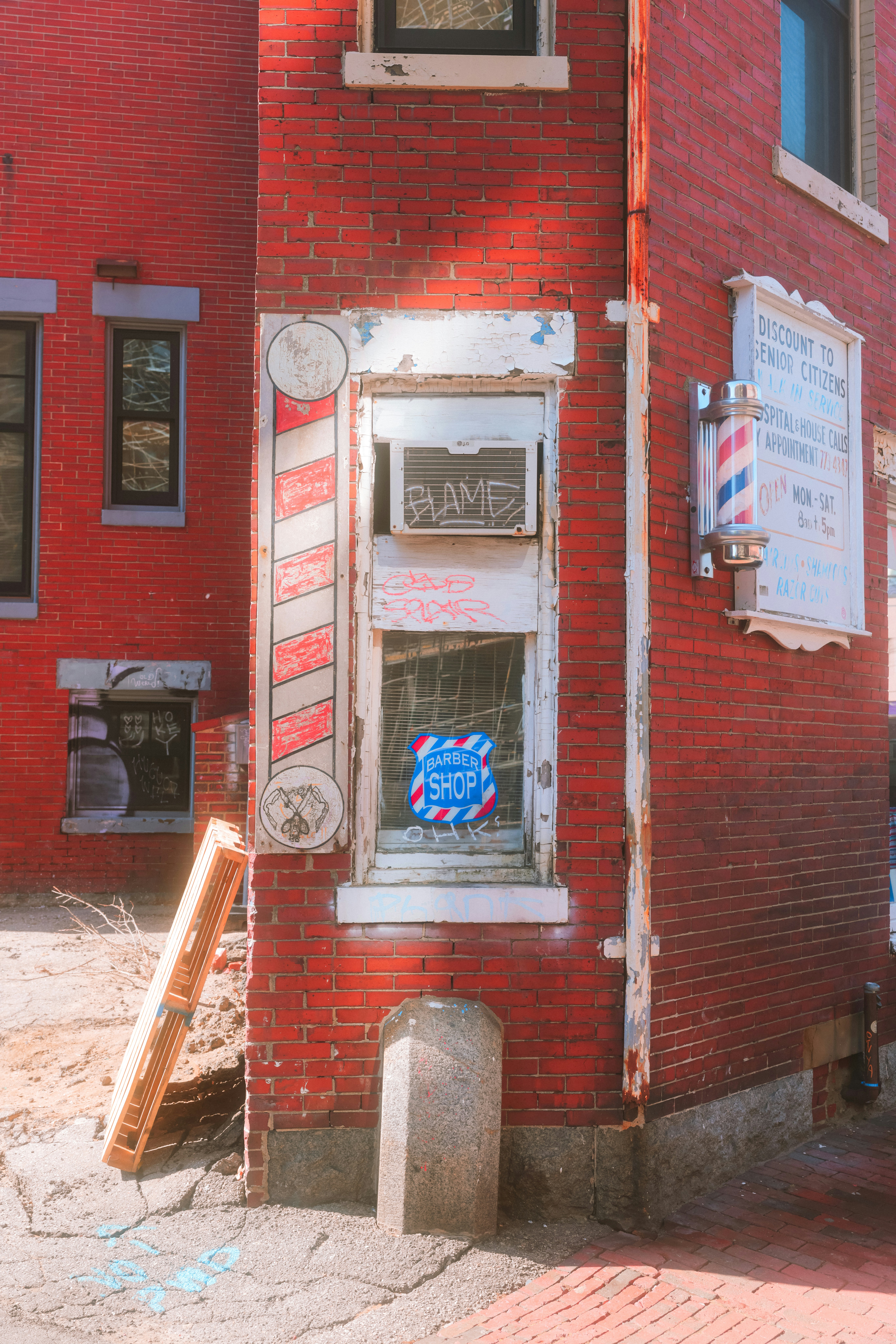Red Brick Barber Shop at a Quiet Corner: Striped Pole, Weathered Window, and Leaning Sign