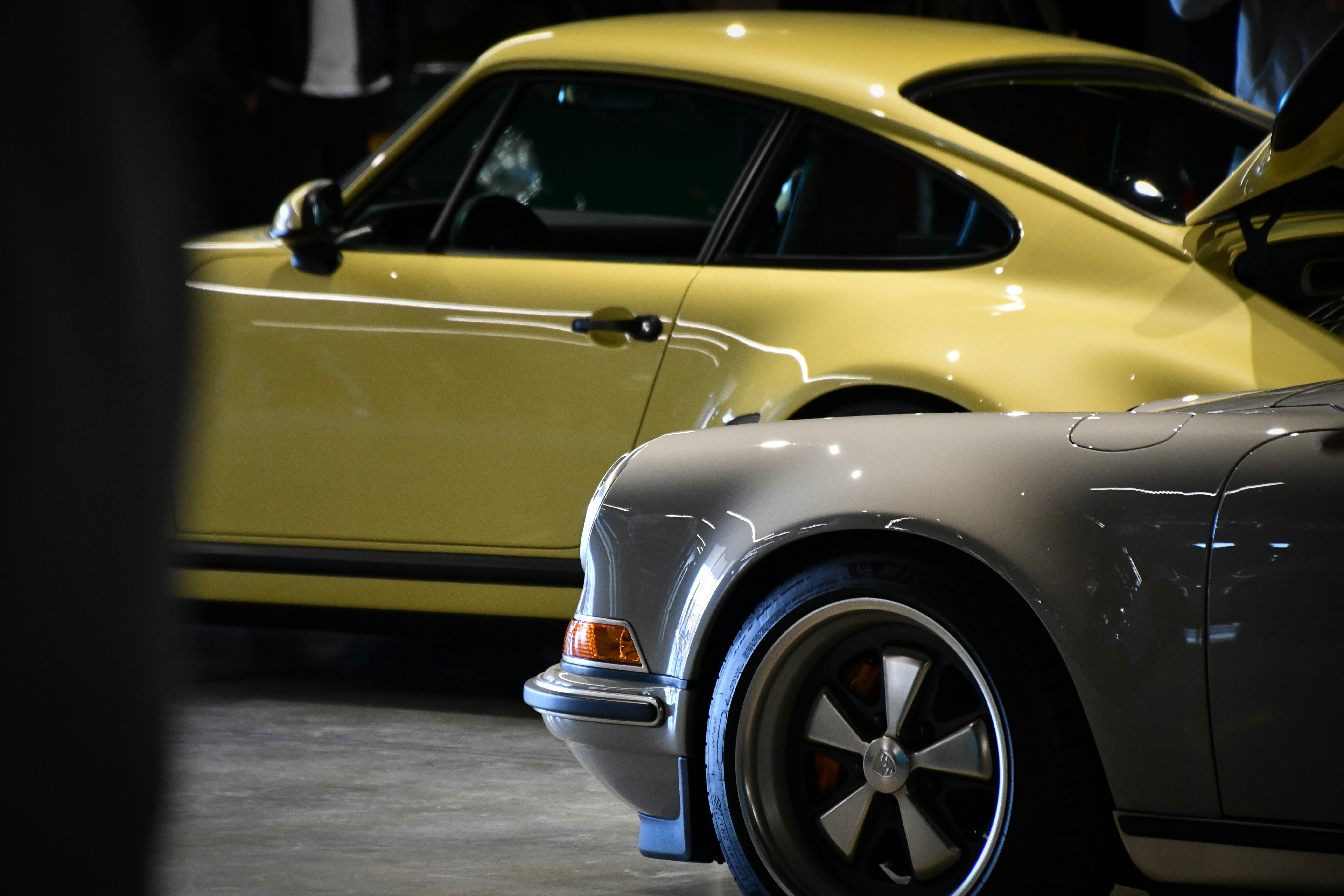 Two iconic Porsche models, one in vibrant yellow and the other in sleek silver, showcased in a modern setting.