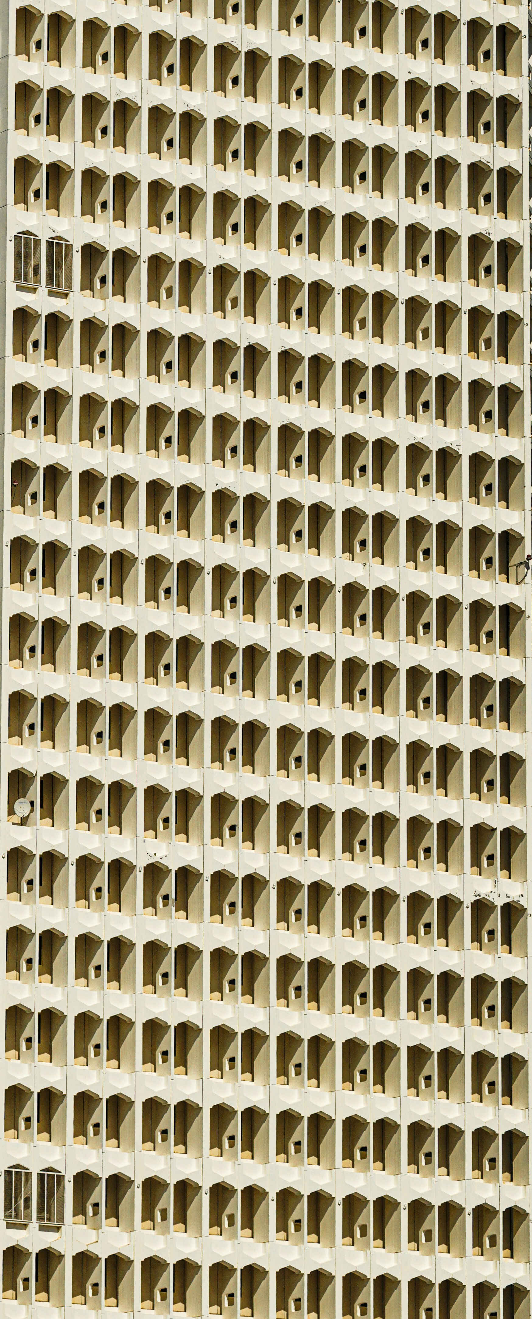 A detailed view of a building facade showcasing a repetitive pattern of arches and windows, emphasizing geometric design. The structure's uniformity creates a striking visual impact.