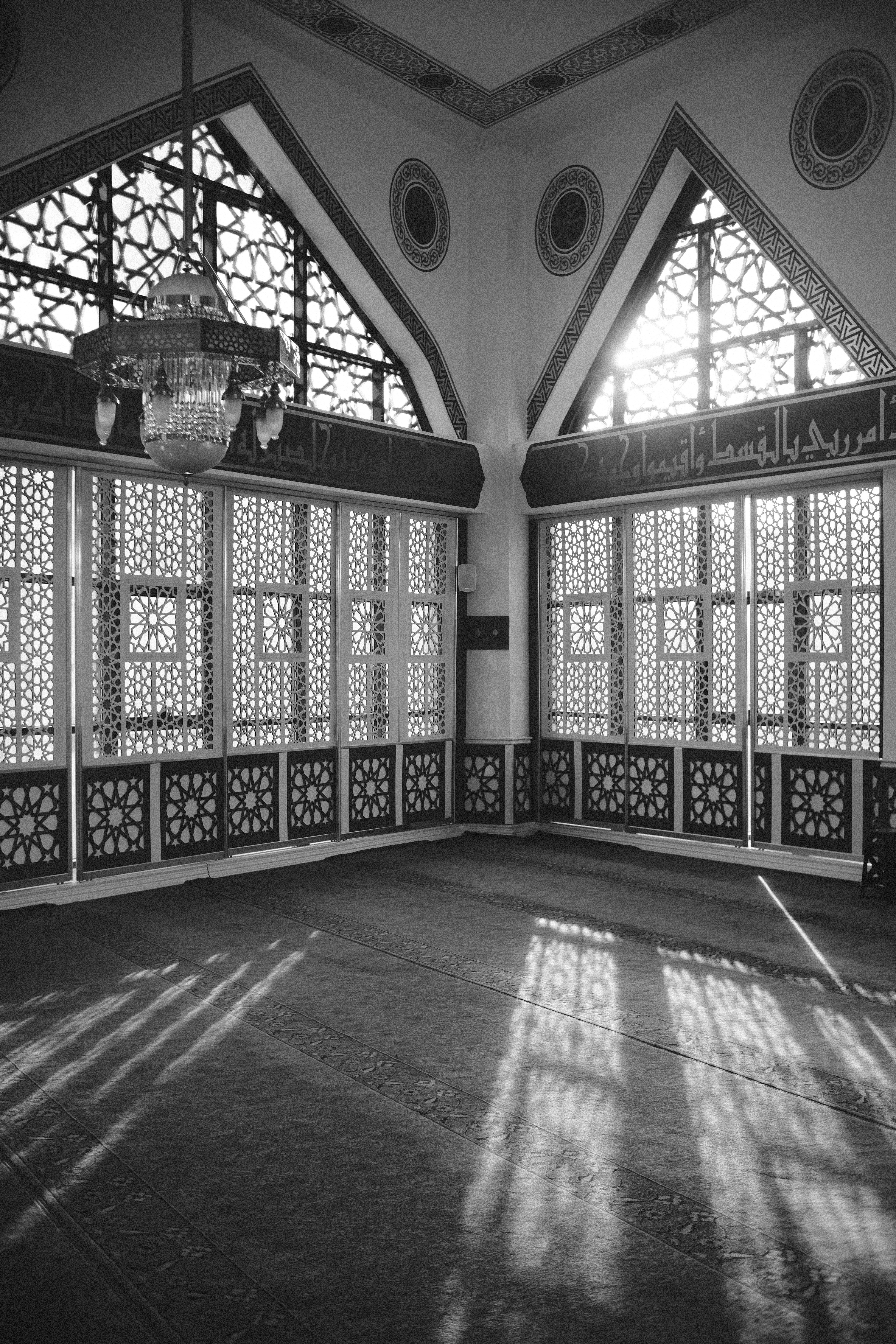 Black and white mosque interior with intricate window patterns casting light on the floor.