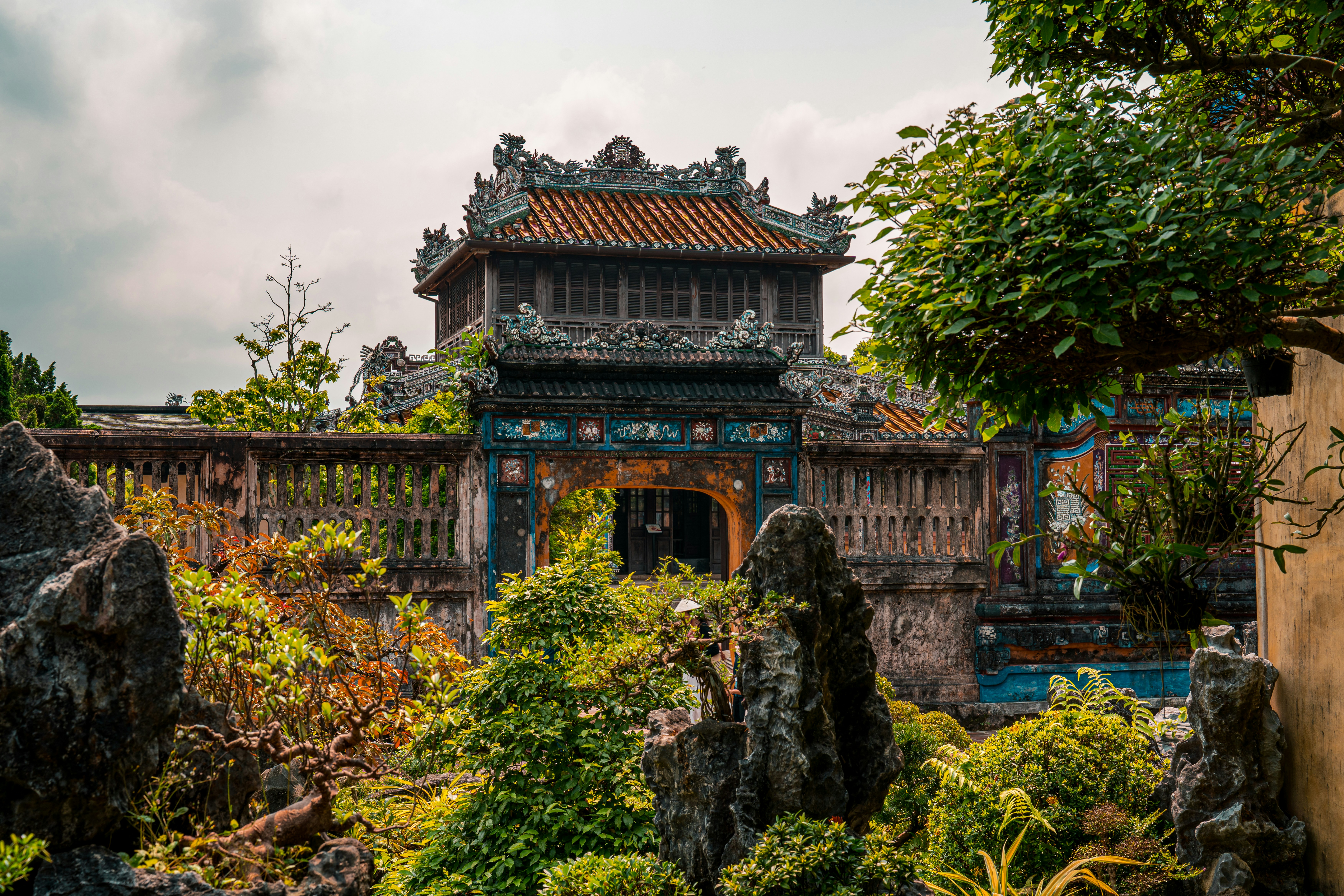 Historic wooden gate framed by lush greenery and ornate stonework under a cloudy sky.