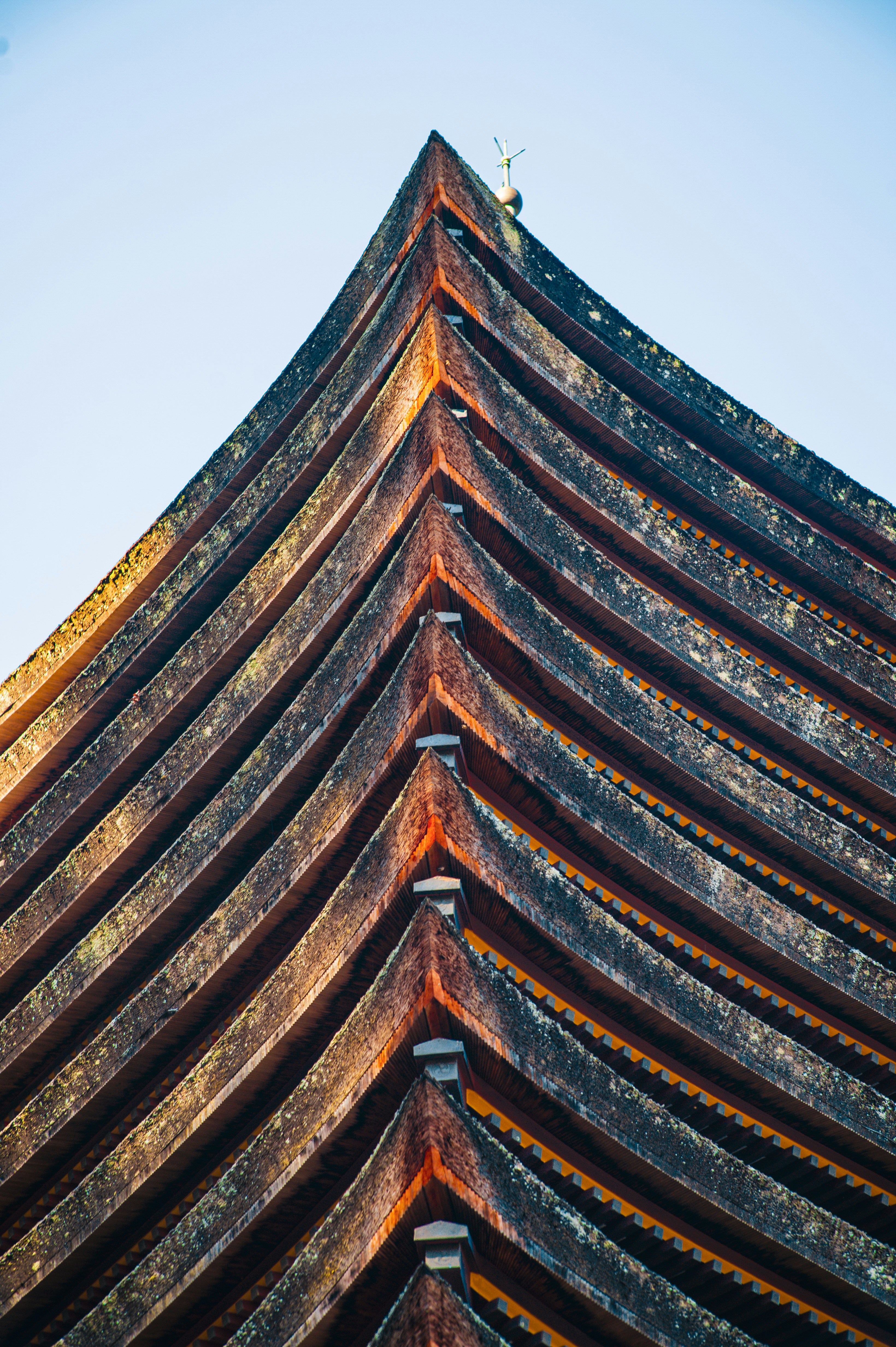 Close-up of a traditional multi-tiered roof with intricate wooden beams, captured against a clear blue sky.