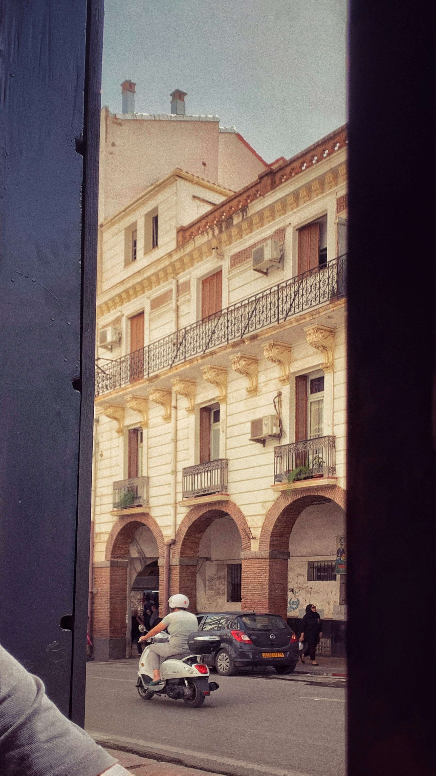 A scooter rider passes by a historic building with arched windows and balconies.