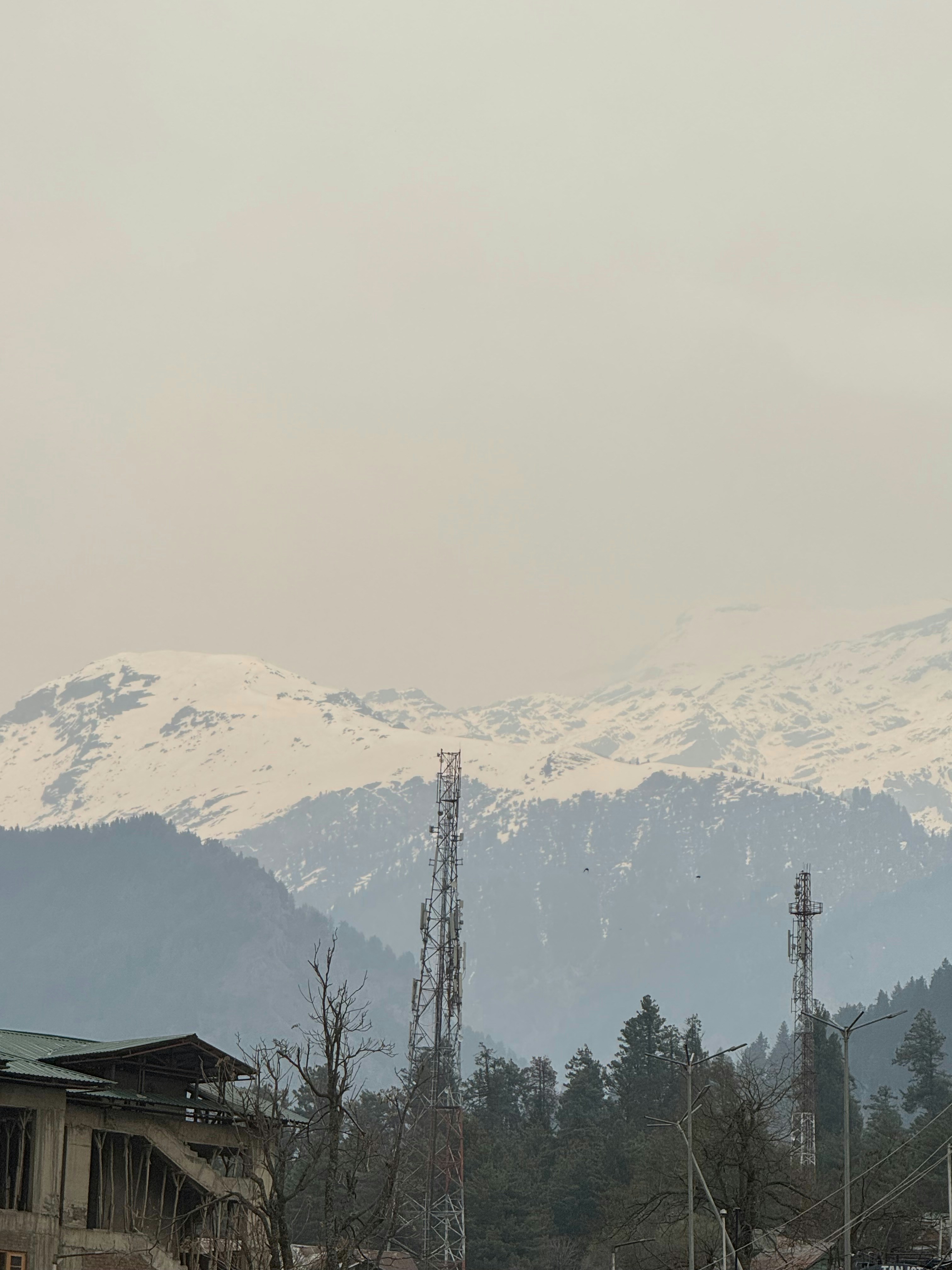 Snow-capped mountains tower over a town with cell towers and buildings in the foreground.