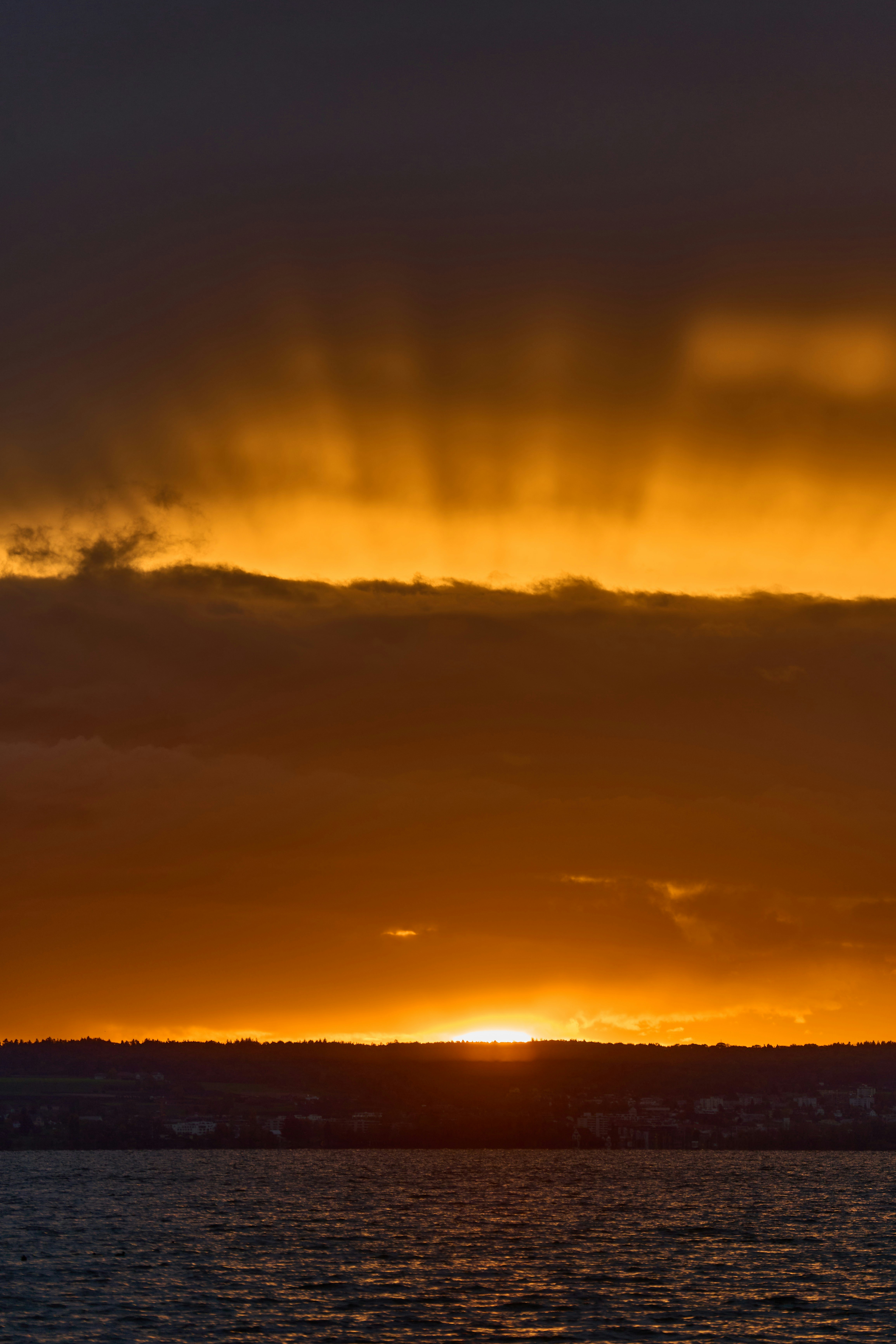 Sunset casting radiant beams through clouds over a calm ocean.