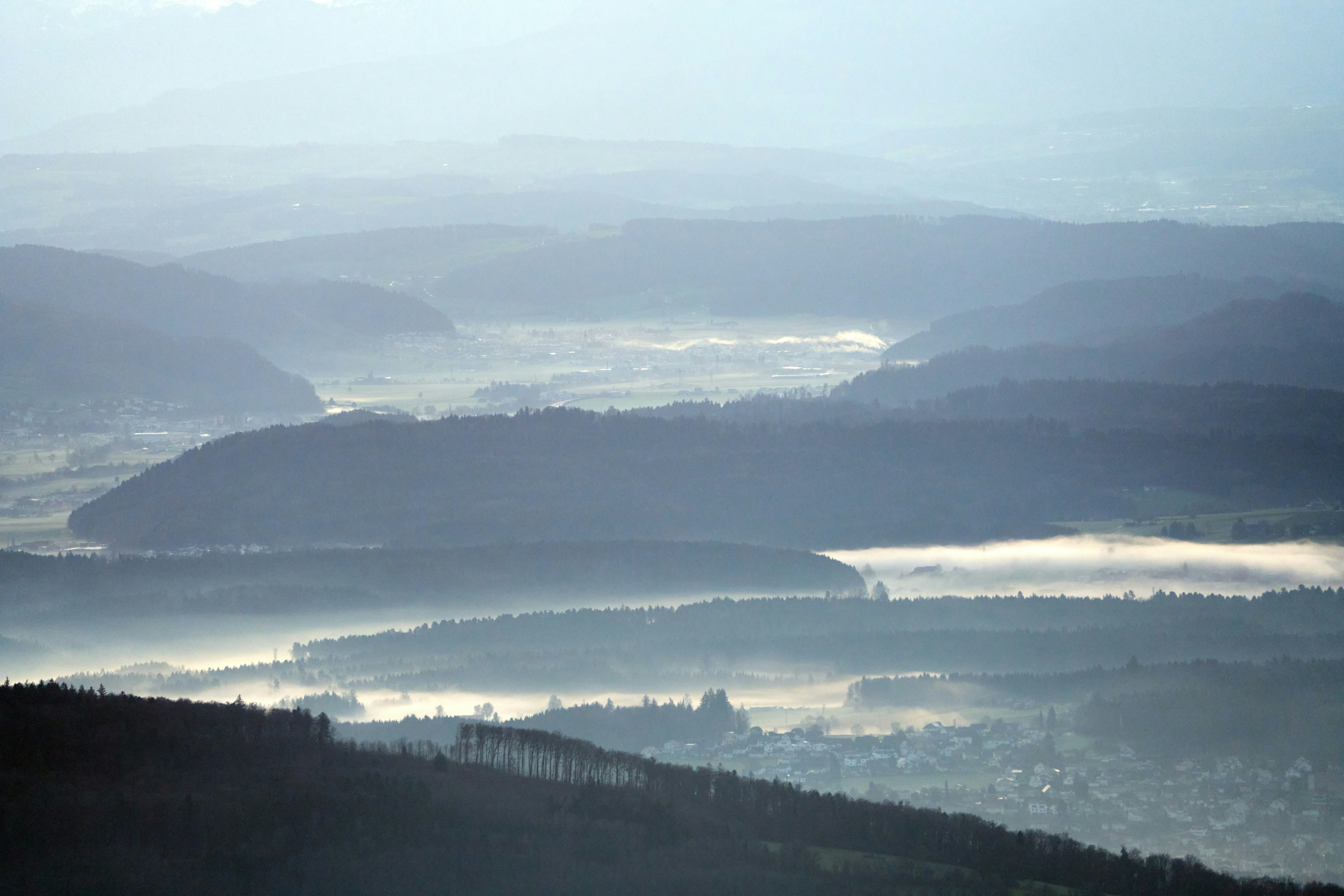 Layers of mist and hills create a serene landscape under soft morning light.