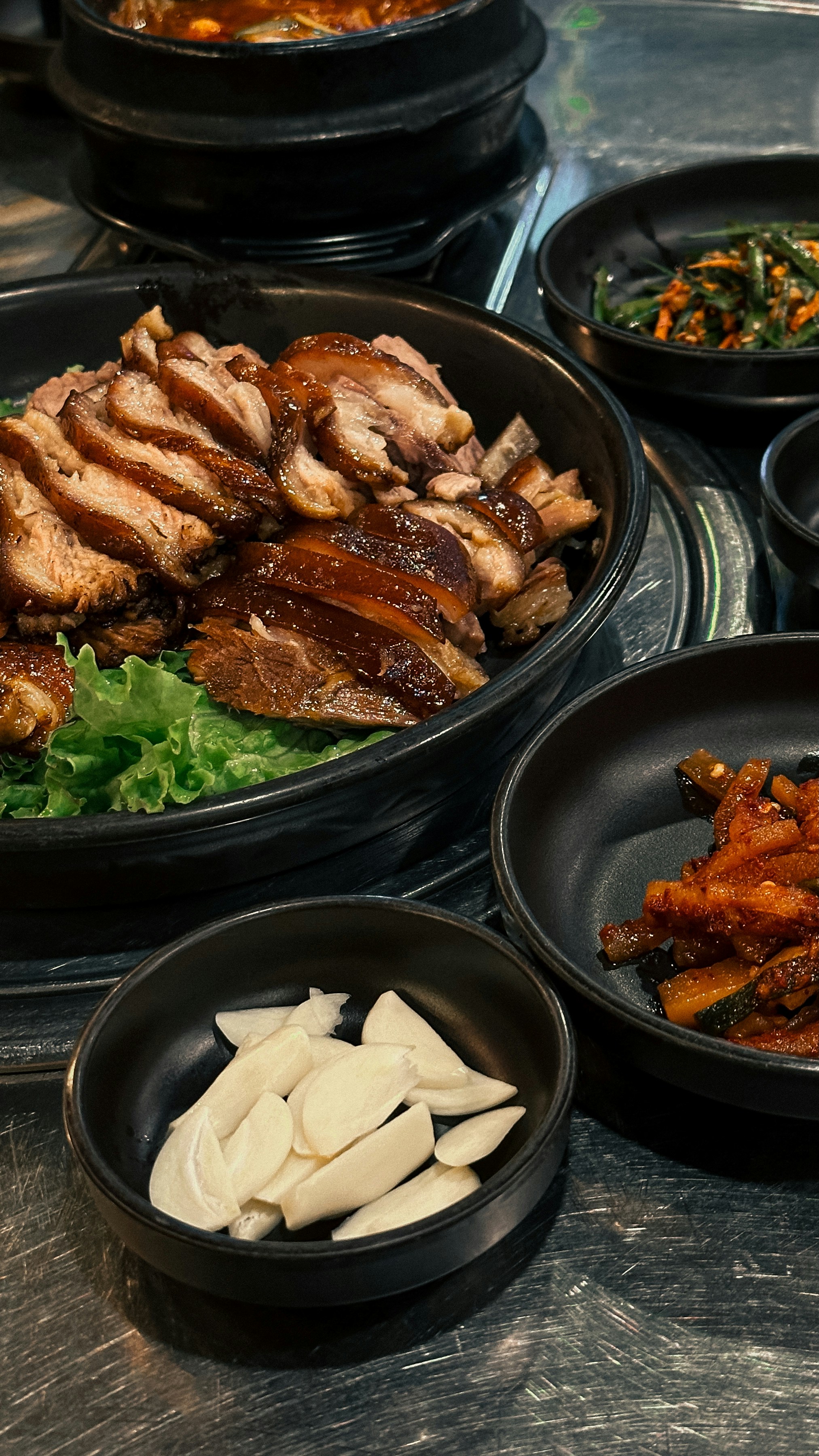 Charred Roast Pork Bowl: Glazed slices crown greens beside a spread of banchan