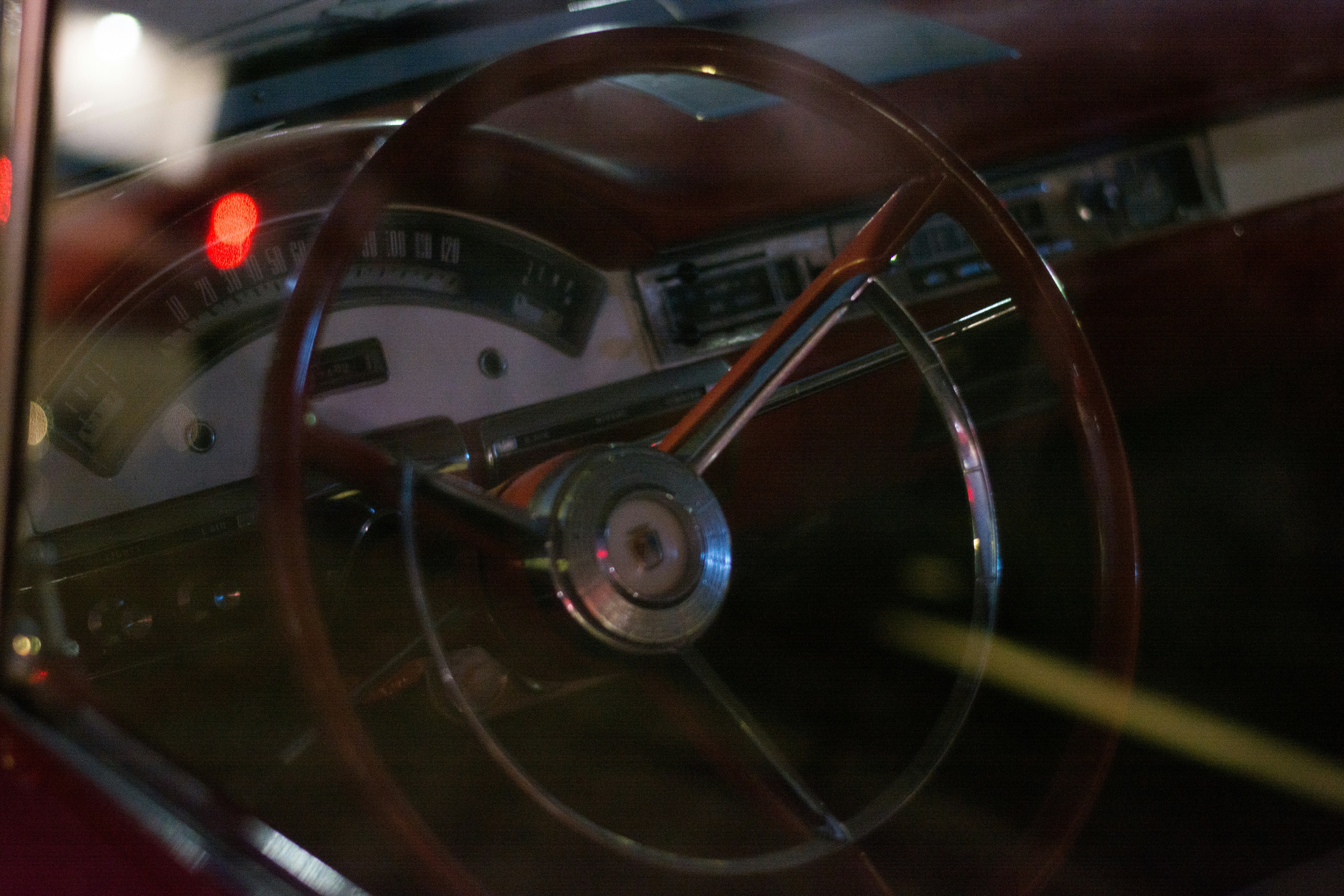 Classic car dashboard featuring a polished steering wheel and vintage gauges, illuminated by ambient light.