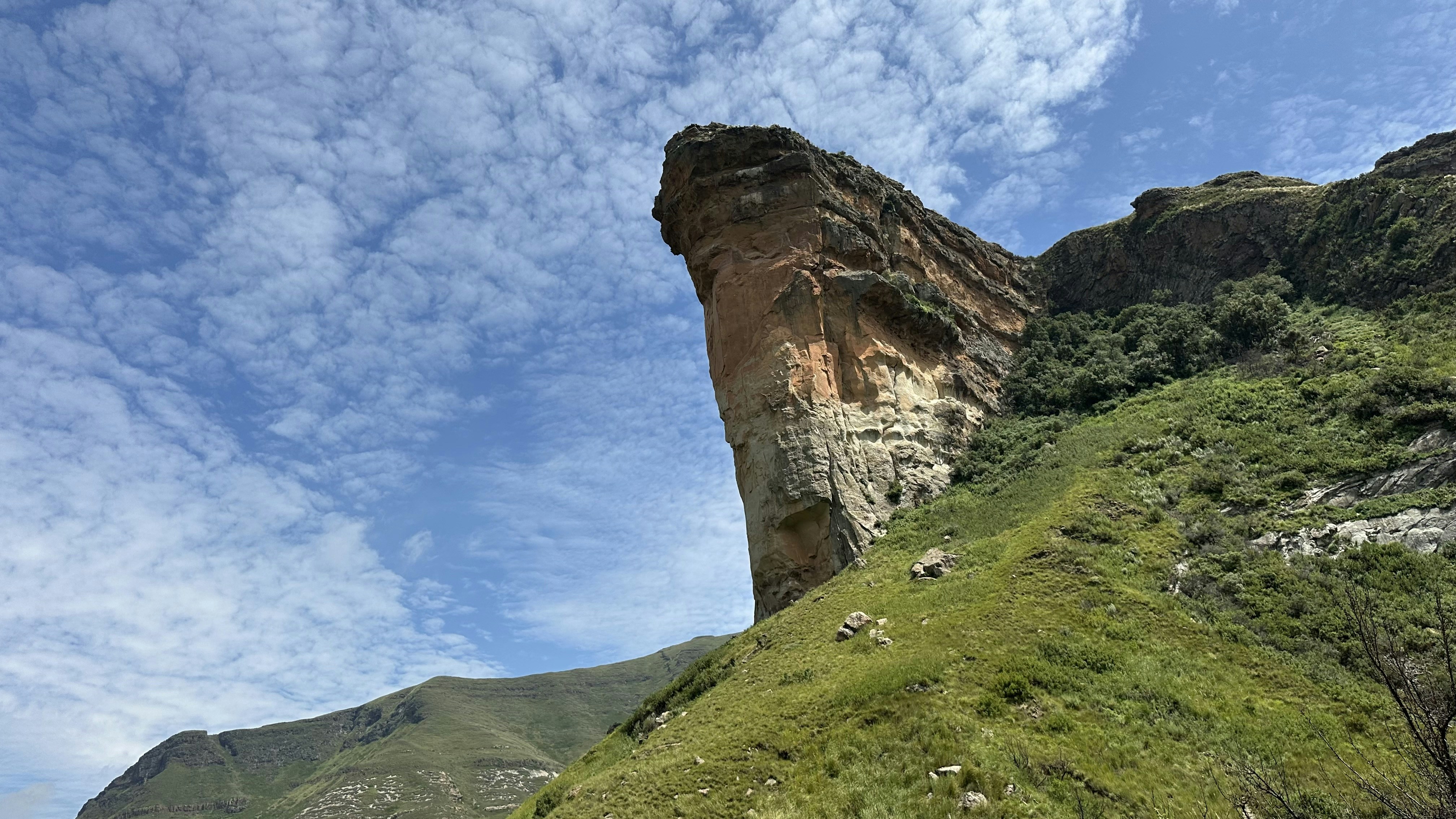 Imposing rock formation towers over a lush green hillside under a vibrant blue sky.