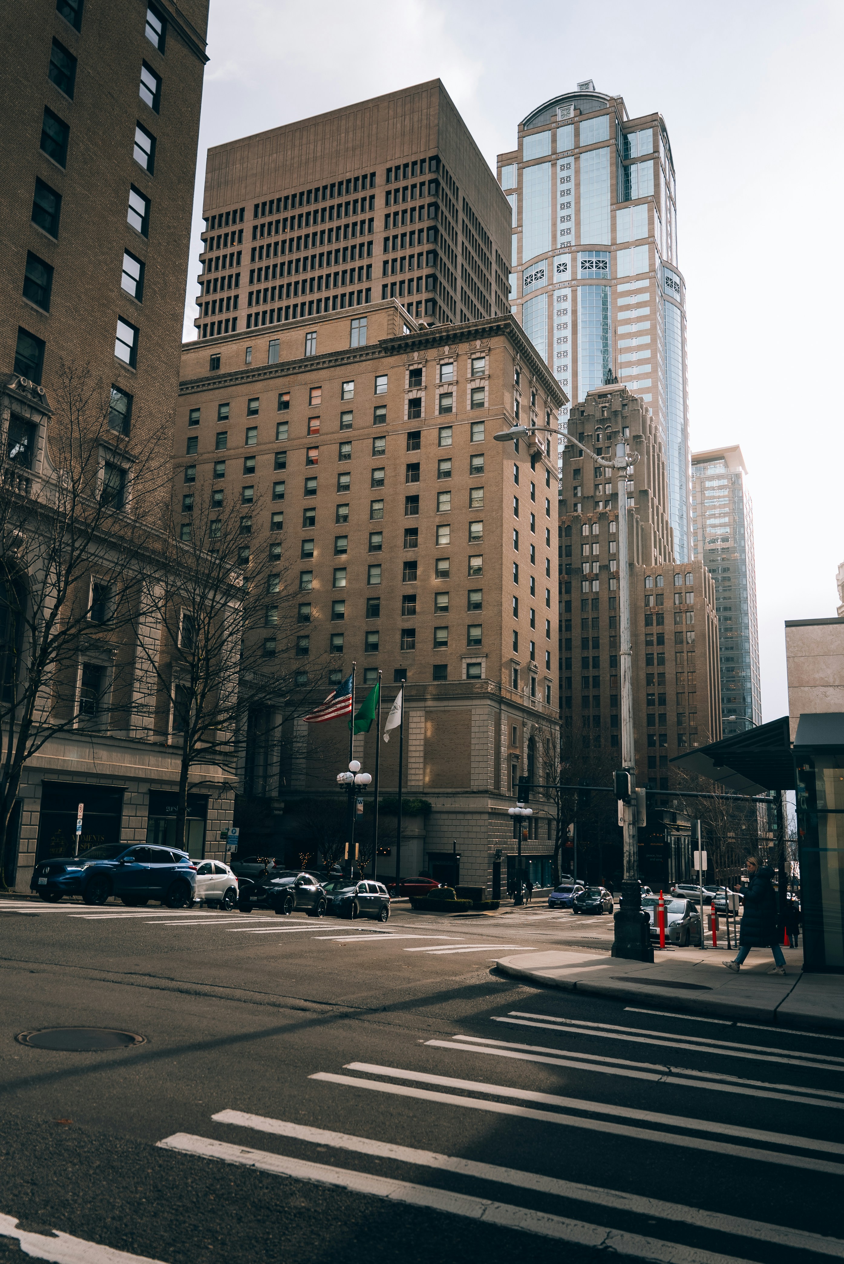 Tall buildings rise along a city street under a partly cloudy sky.
