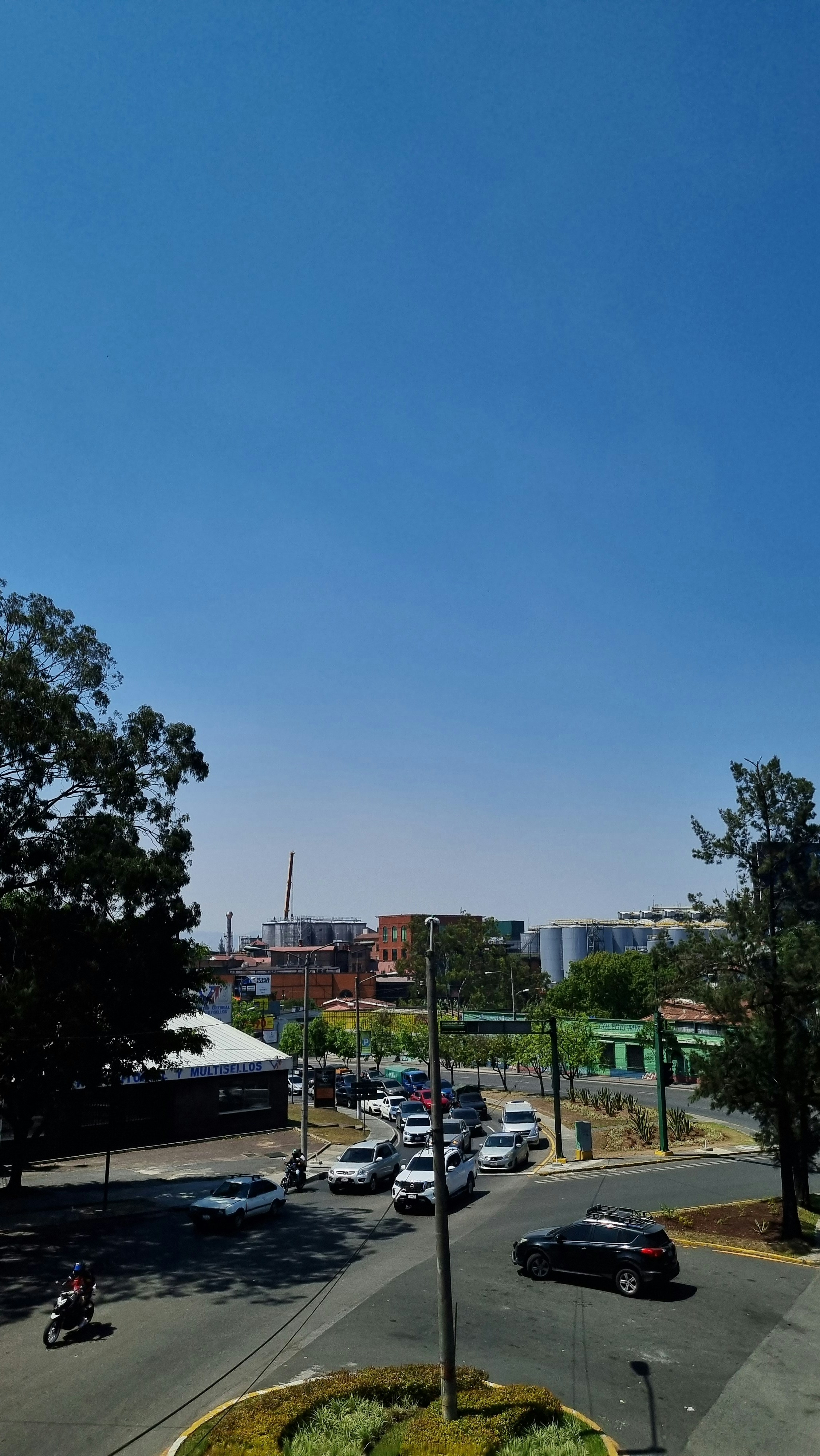 Busy city intersection with cars and trees under a bright blue sky.