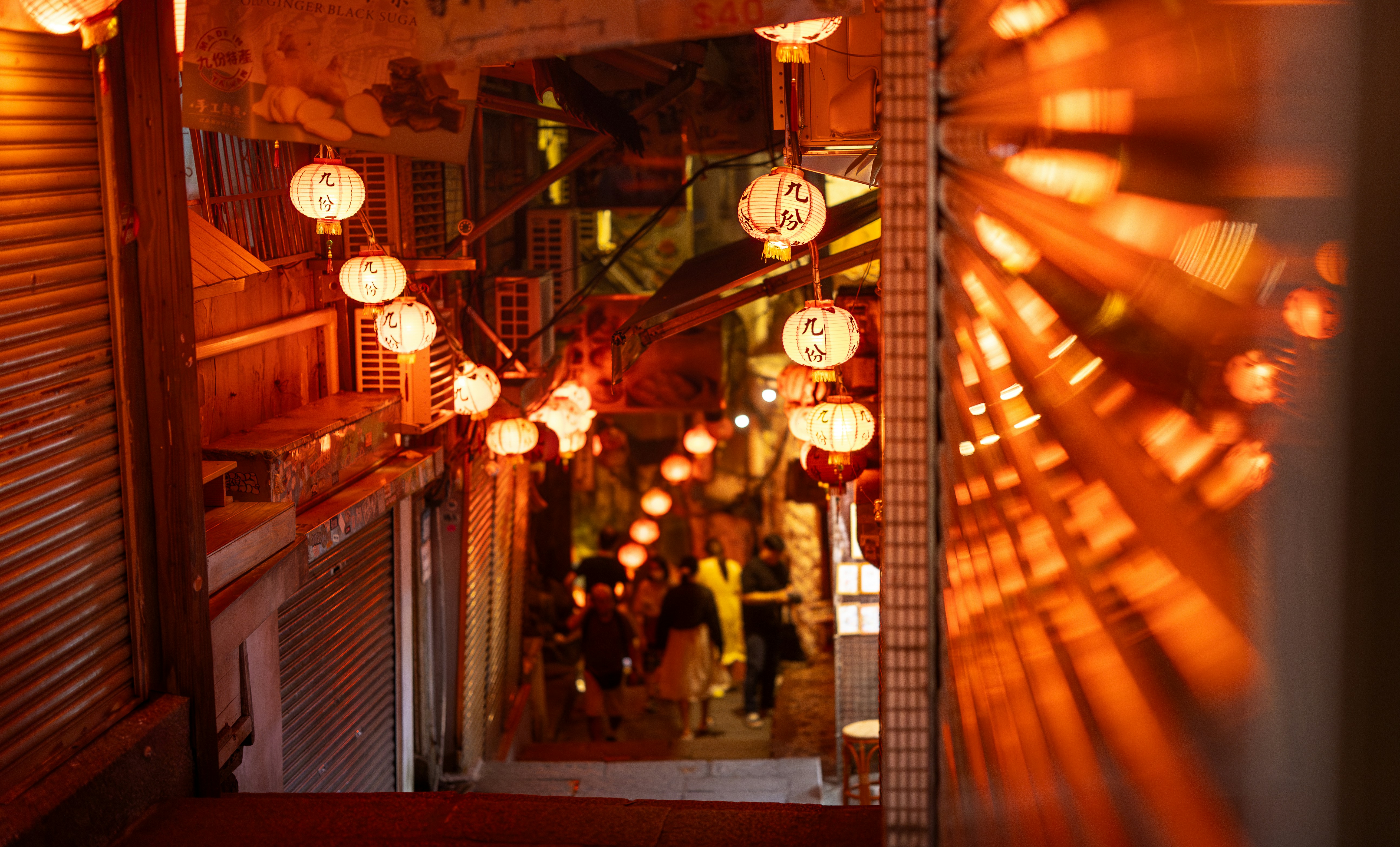 Warmly lit alley adorned with red lanterns reflecting off metallic surfaces.
