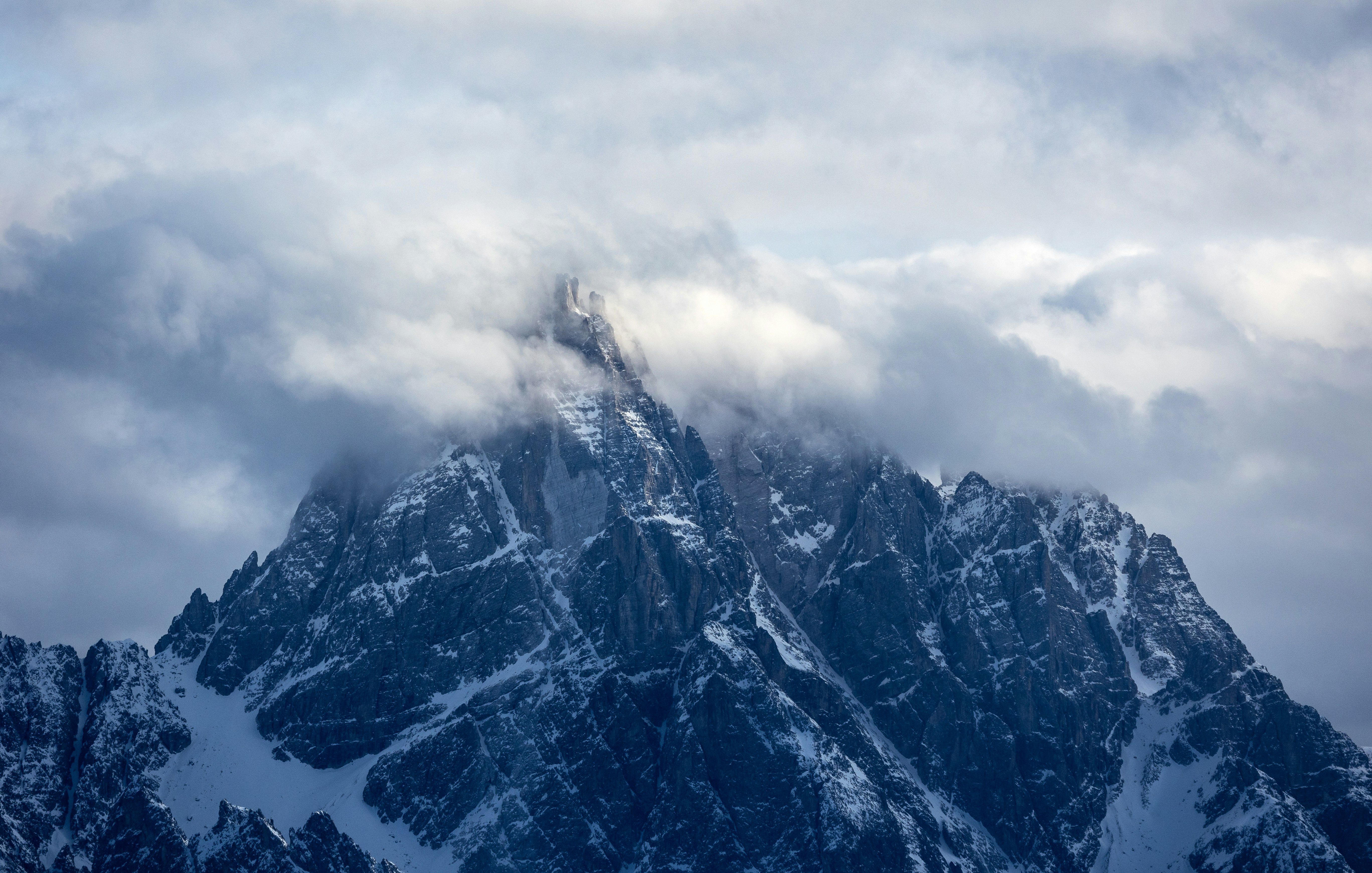 Snow-capped mountain peak shrouded in swirling clouds under a moody sky.