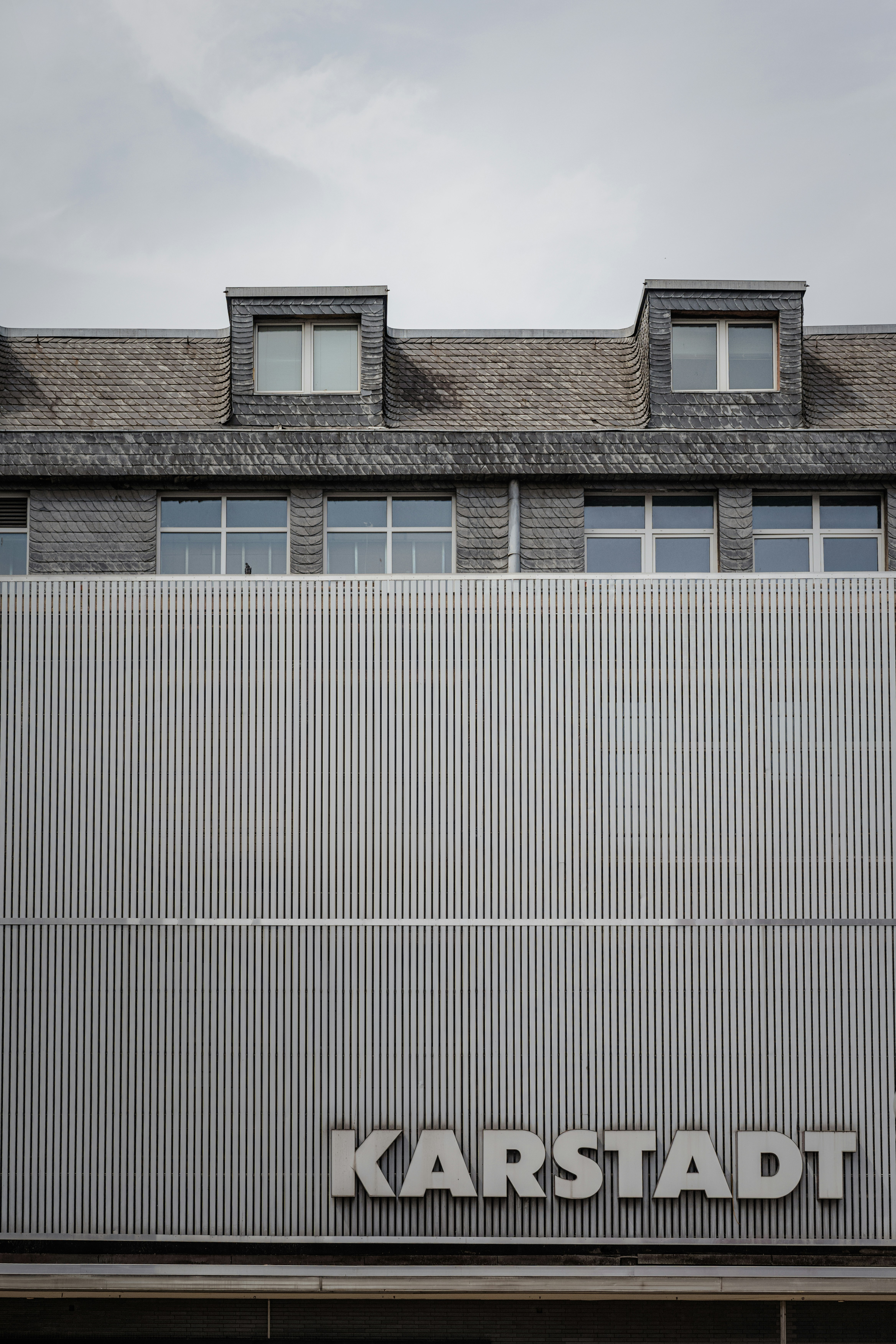 Facade of a building with a minimalist design, featuring the name 'Karstadt' and dormer windows under a cloudy sky.