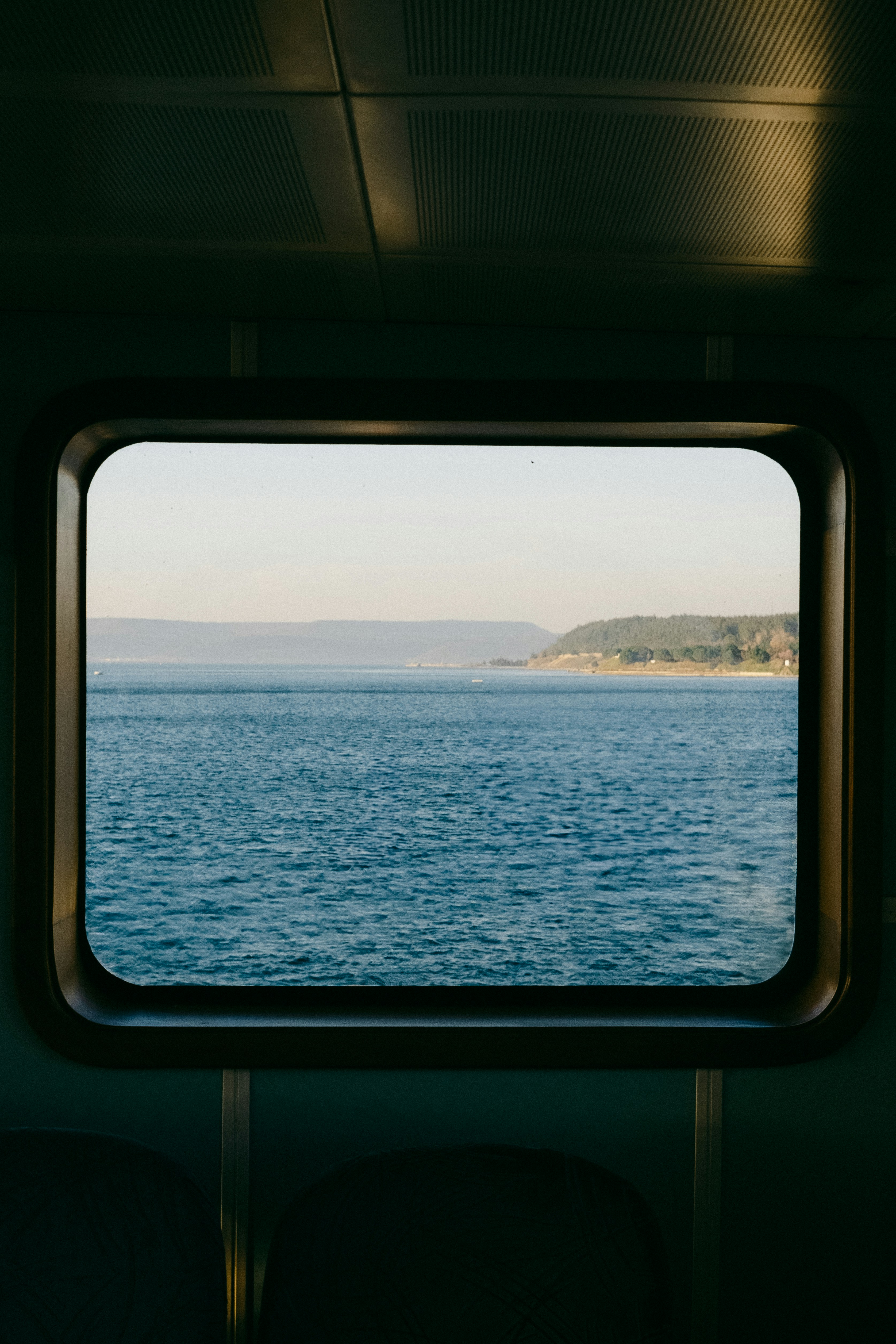 View of a tranquil seascape through a window, showcasing calm waters and distant hills. The scene captures a moment of peace and reflection.