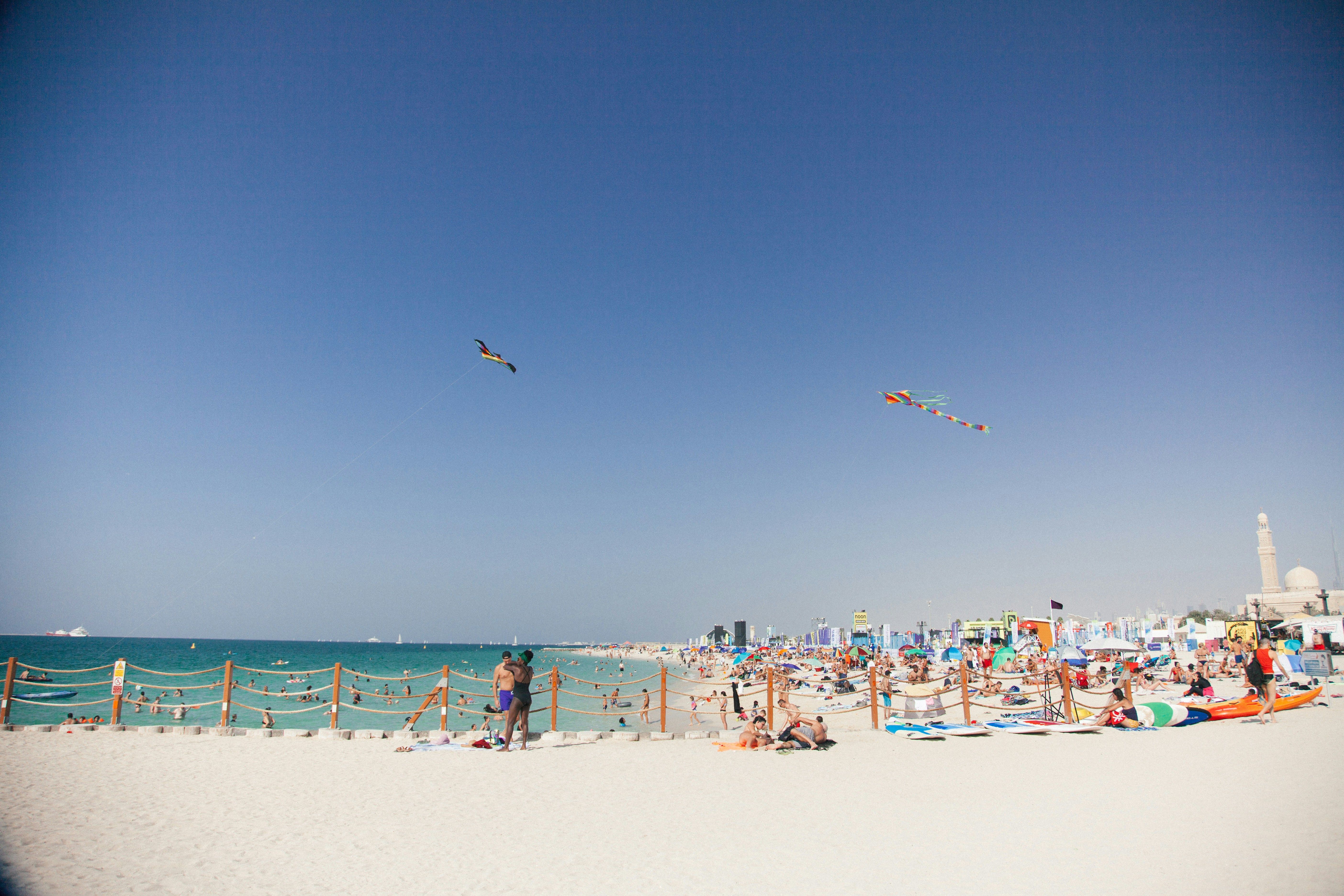 Crowded beach scene with people enjoying the sun and sea under a clear blue sky.