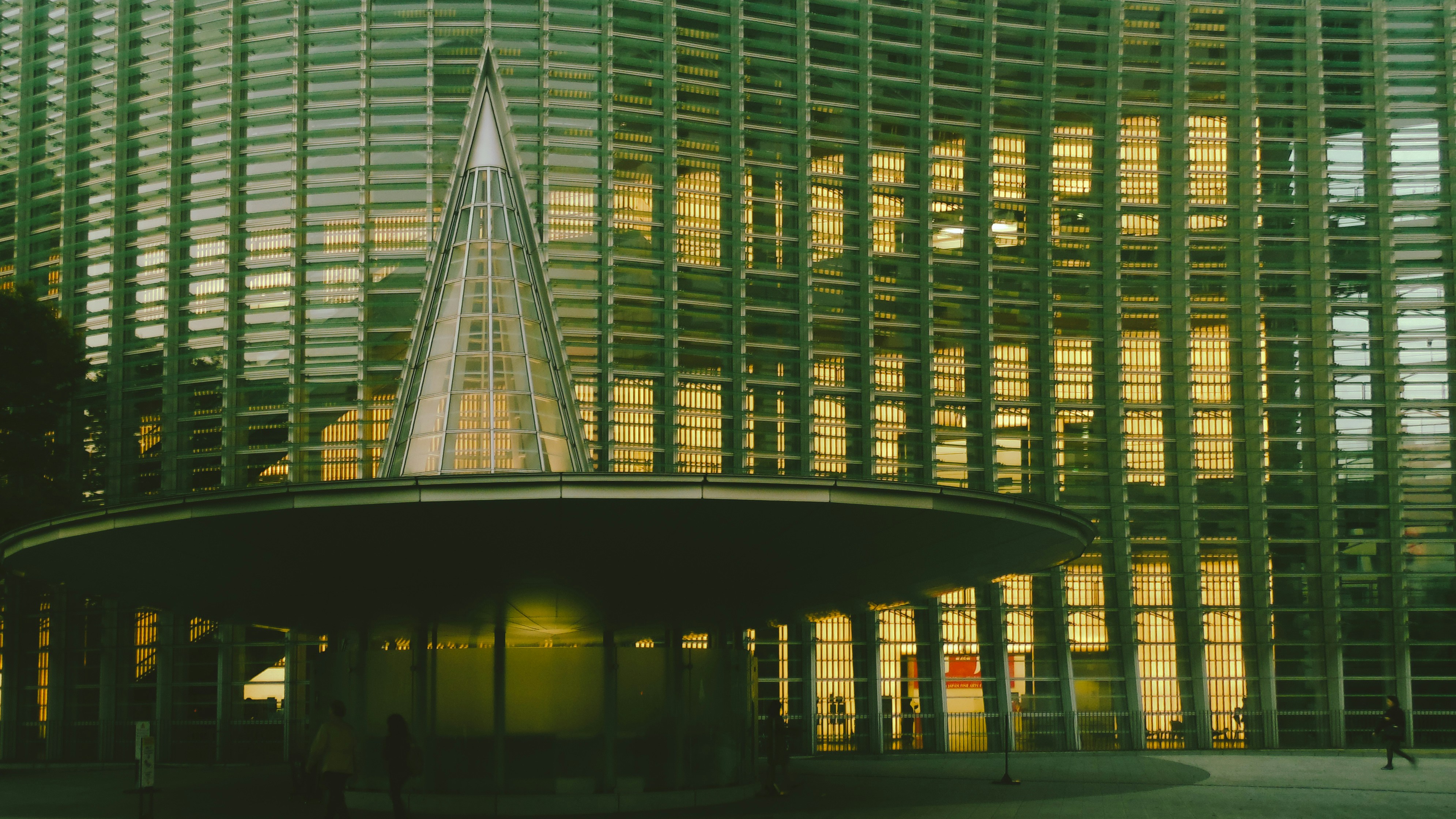 Modern architectural facade with illuminated glass panels and a conical structure at the National Art Center Tokyo.