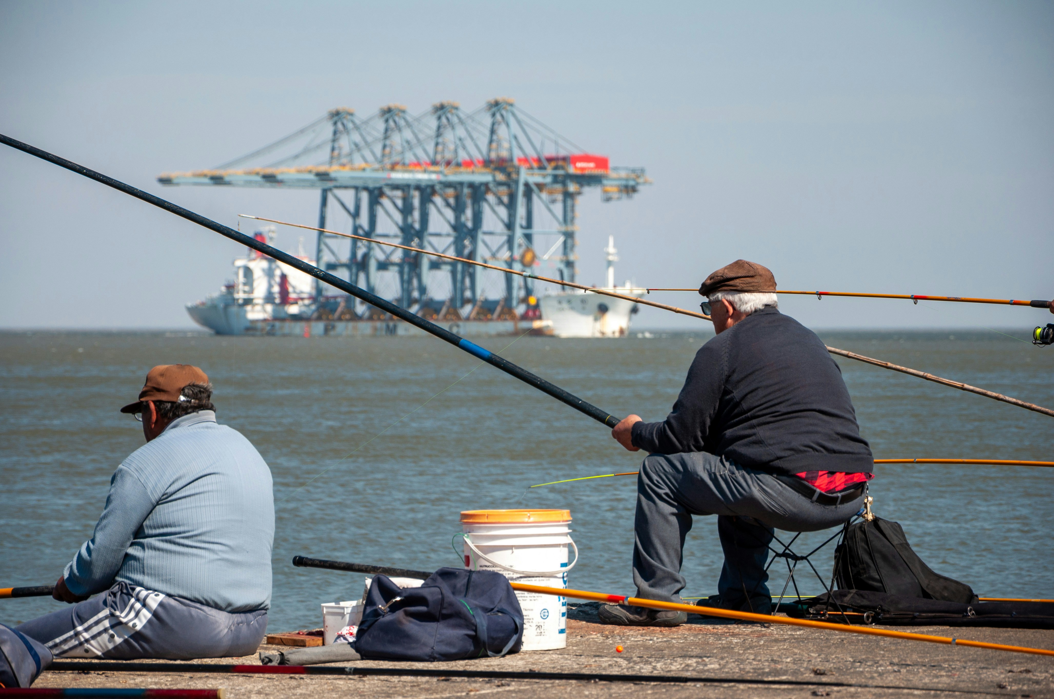 Men fish near industrial cranes in the water. photo – Free Fishing ...