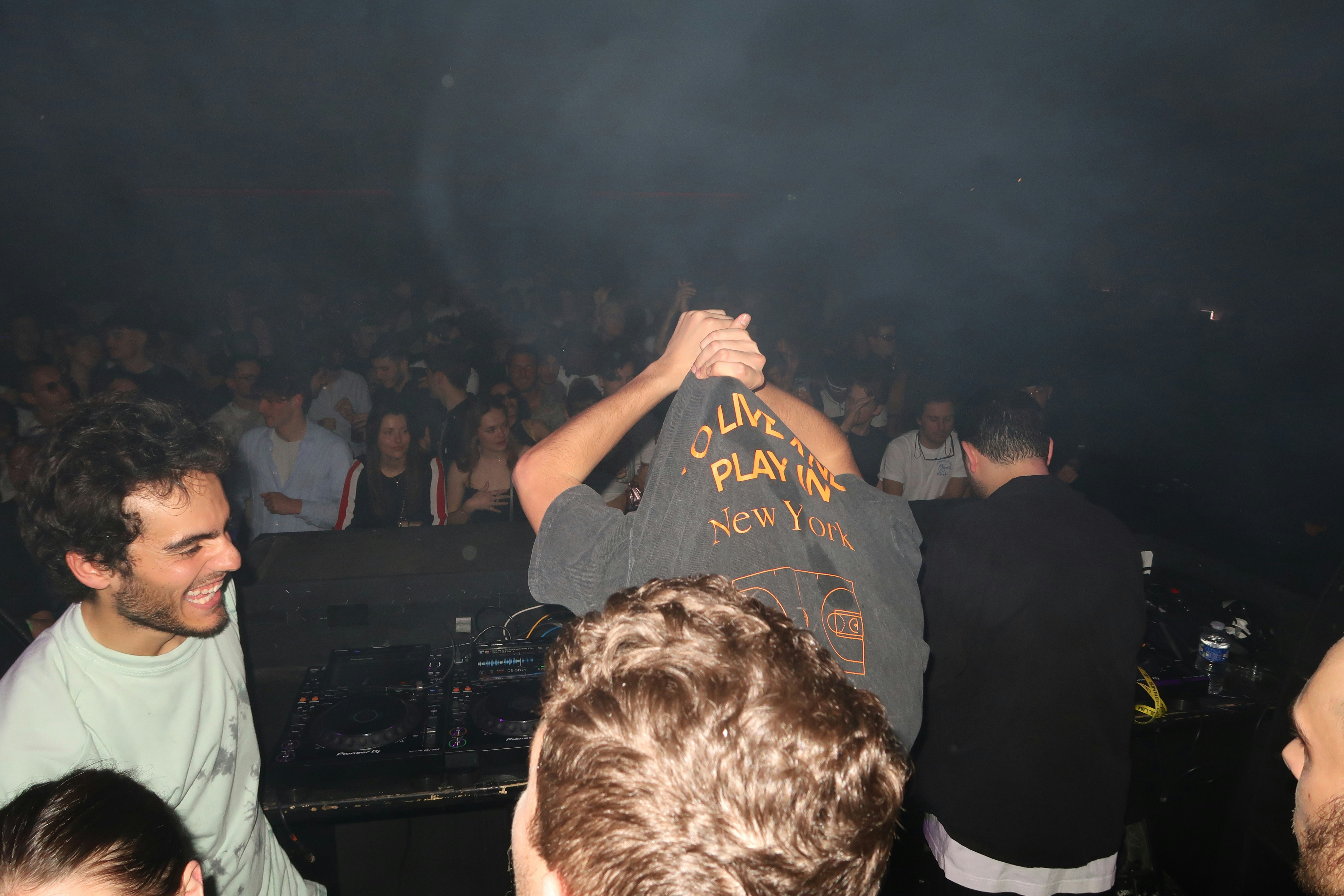 DJ interacts with an energetic crowd in a dimly lit club.