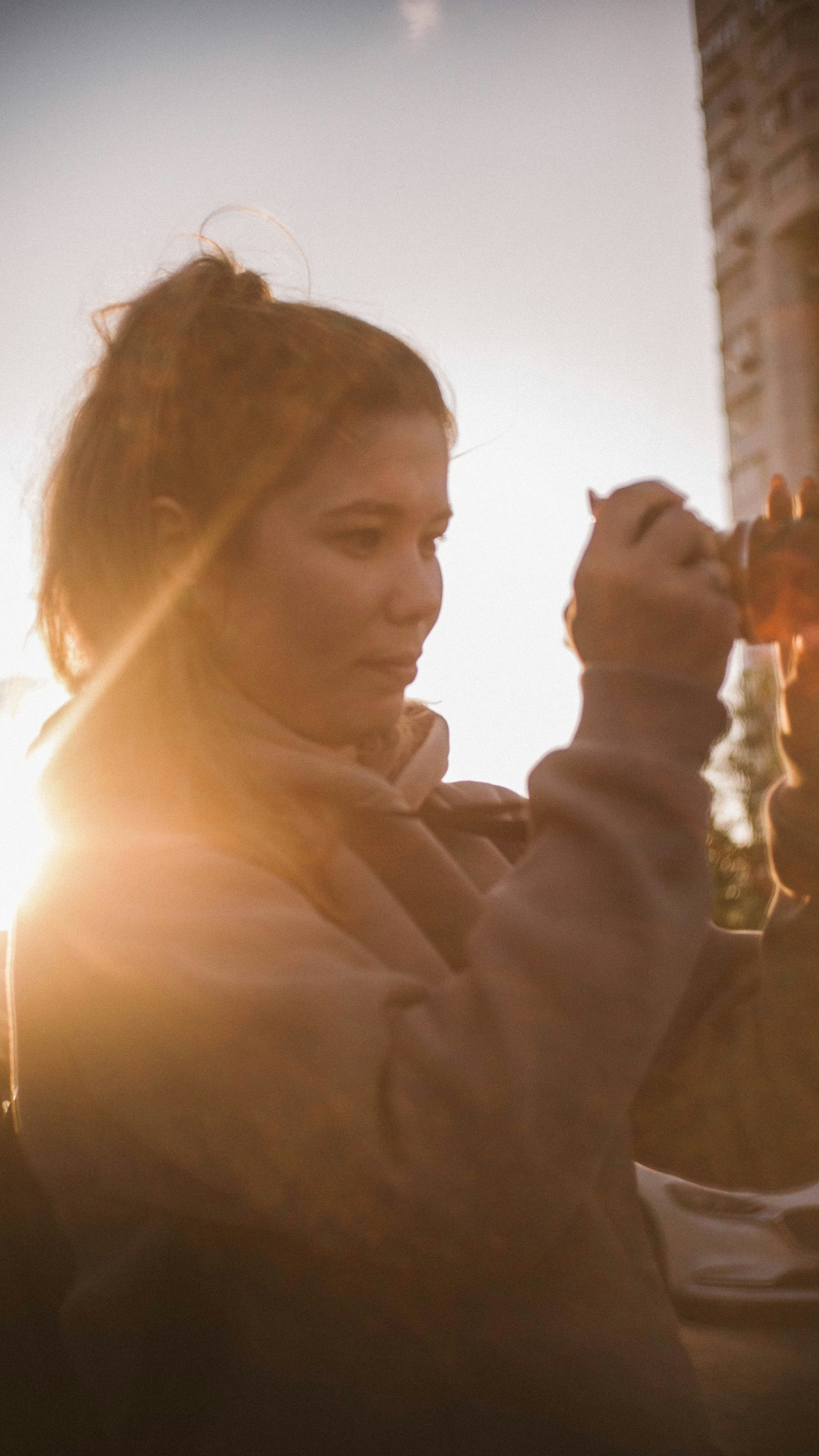 Person in a hoodie photographing with a smartphone against a sunlit urban backdrop.