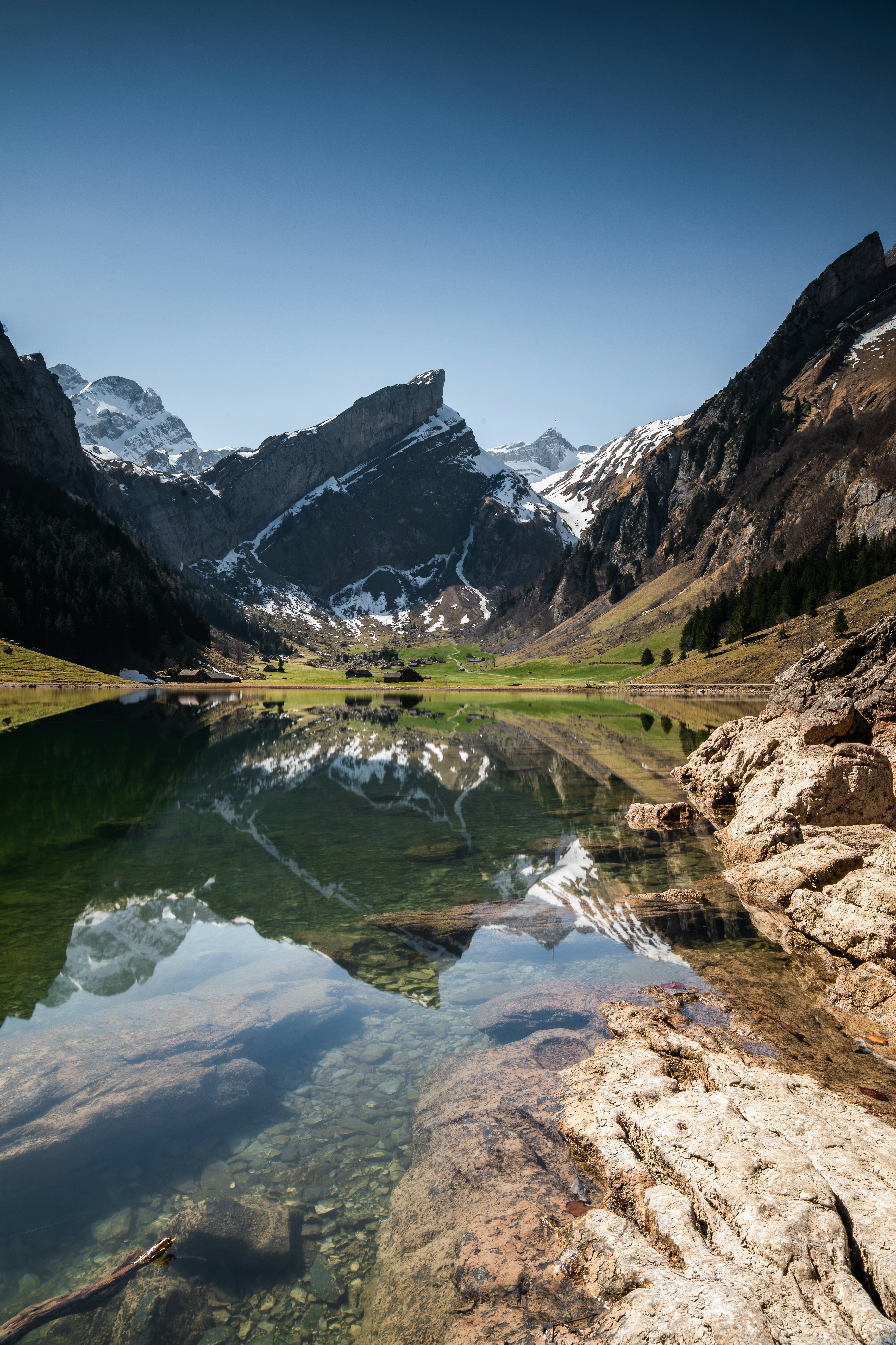 Clear mountain lake reflecting rugged peaks and blue sky.