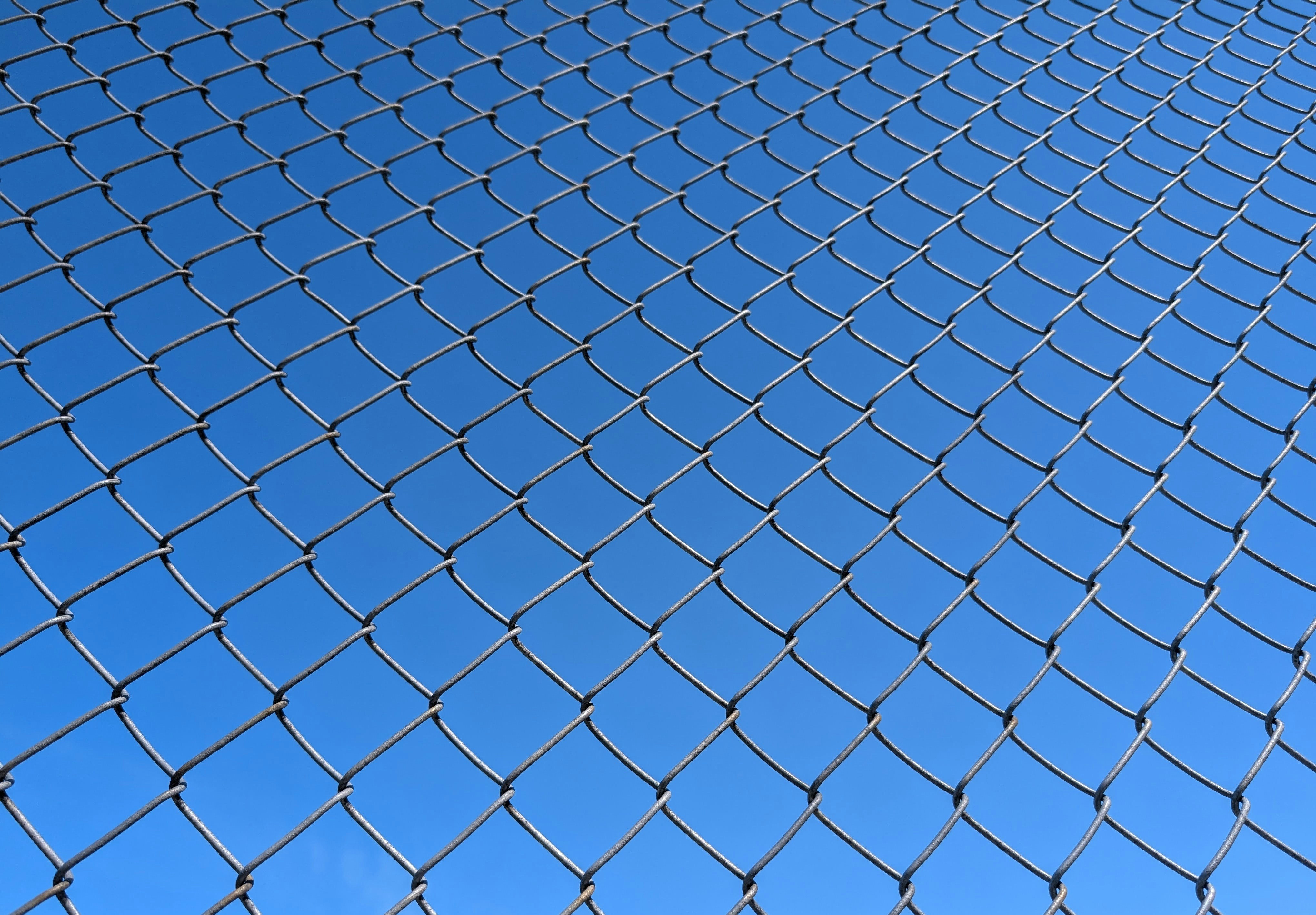 Chain-link fence stretching diagonally across a clear blue sky.