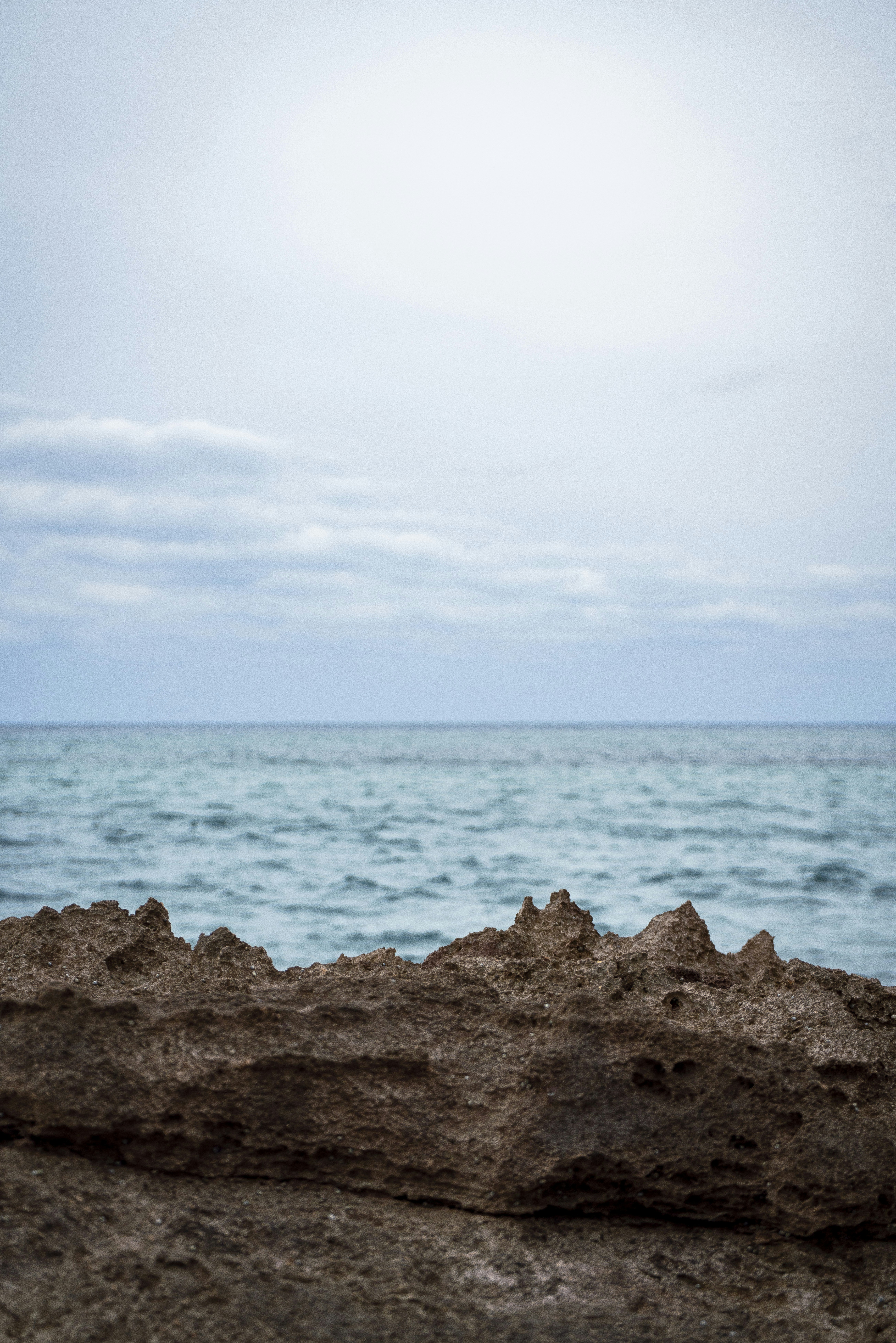 Jagged rocks edge a tranquil sea beneath a softly clouded sky.