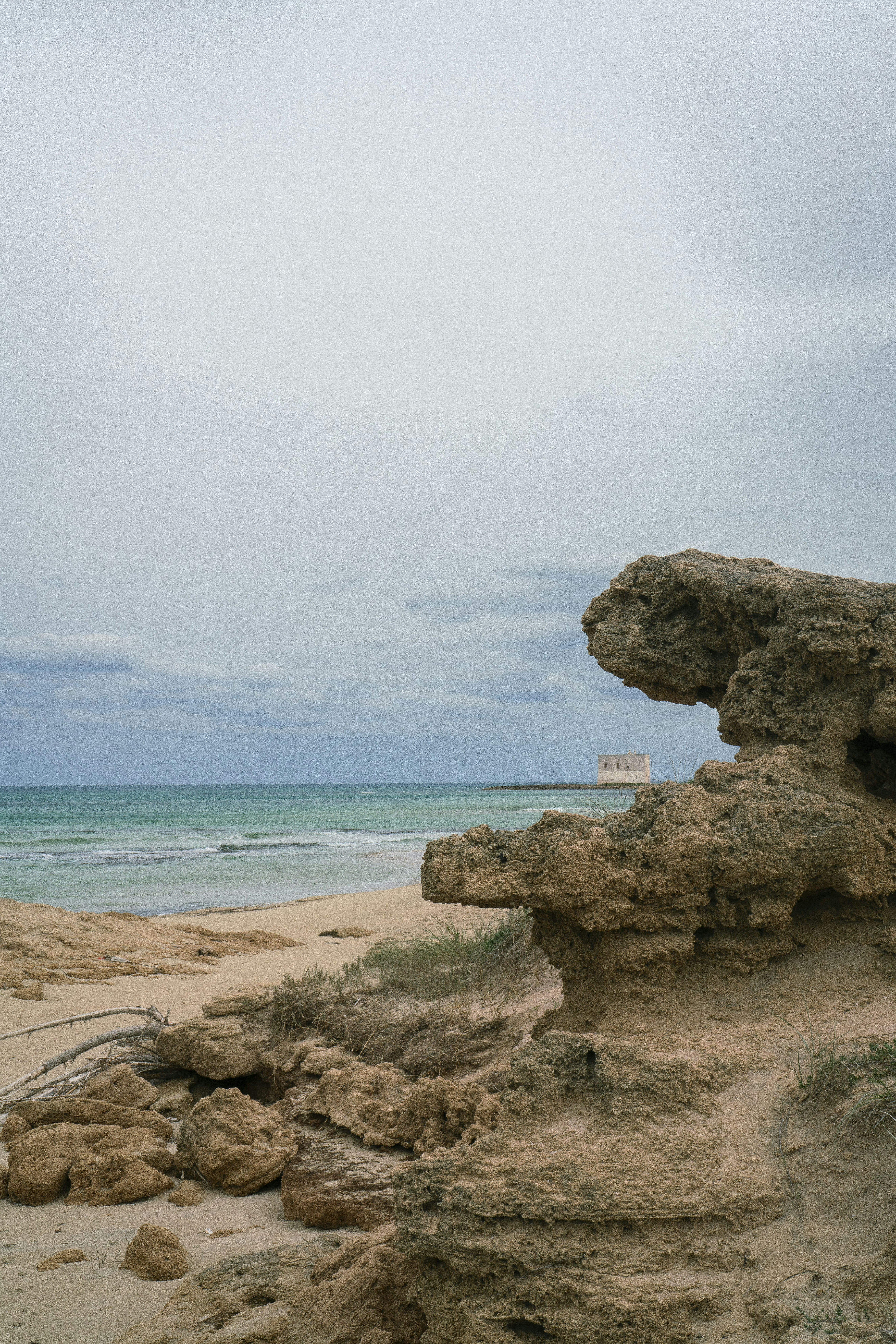 Weathered rock formation overlooking a sandy beach and turquoise ocean under a cloudy sky.