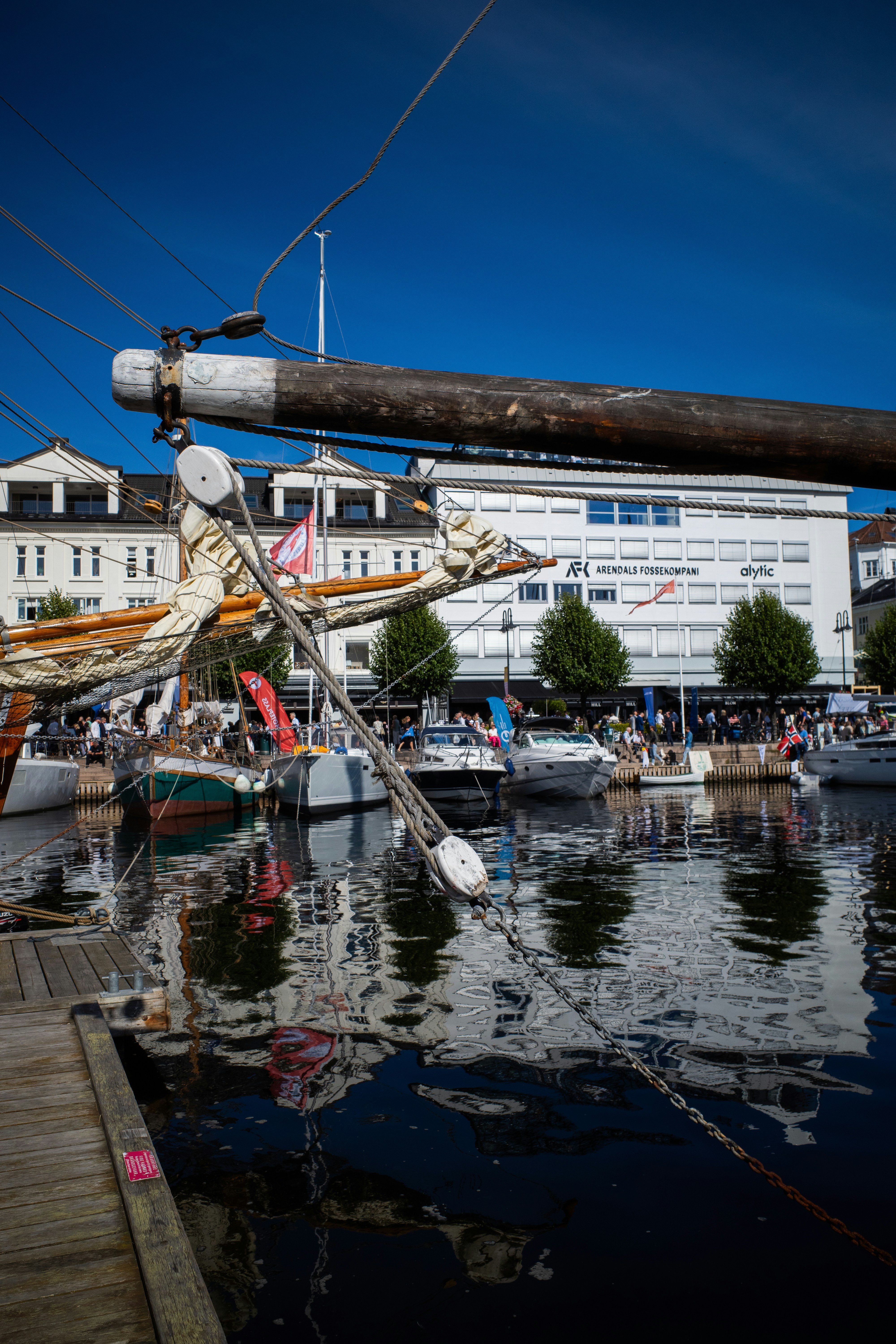Sailboats docked at Arendal harbor with clear blue skies and reflections in the water.
