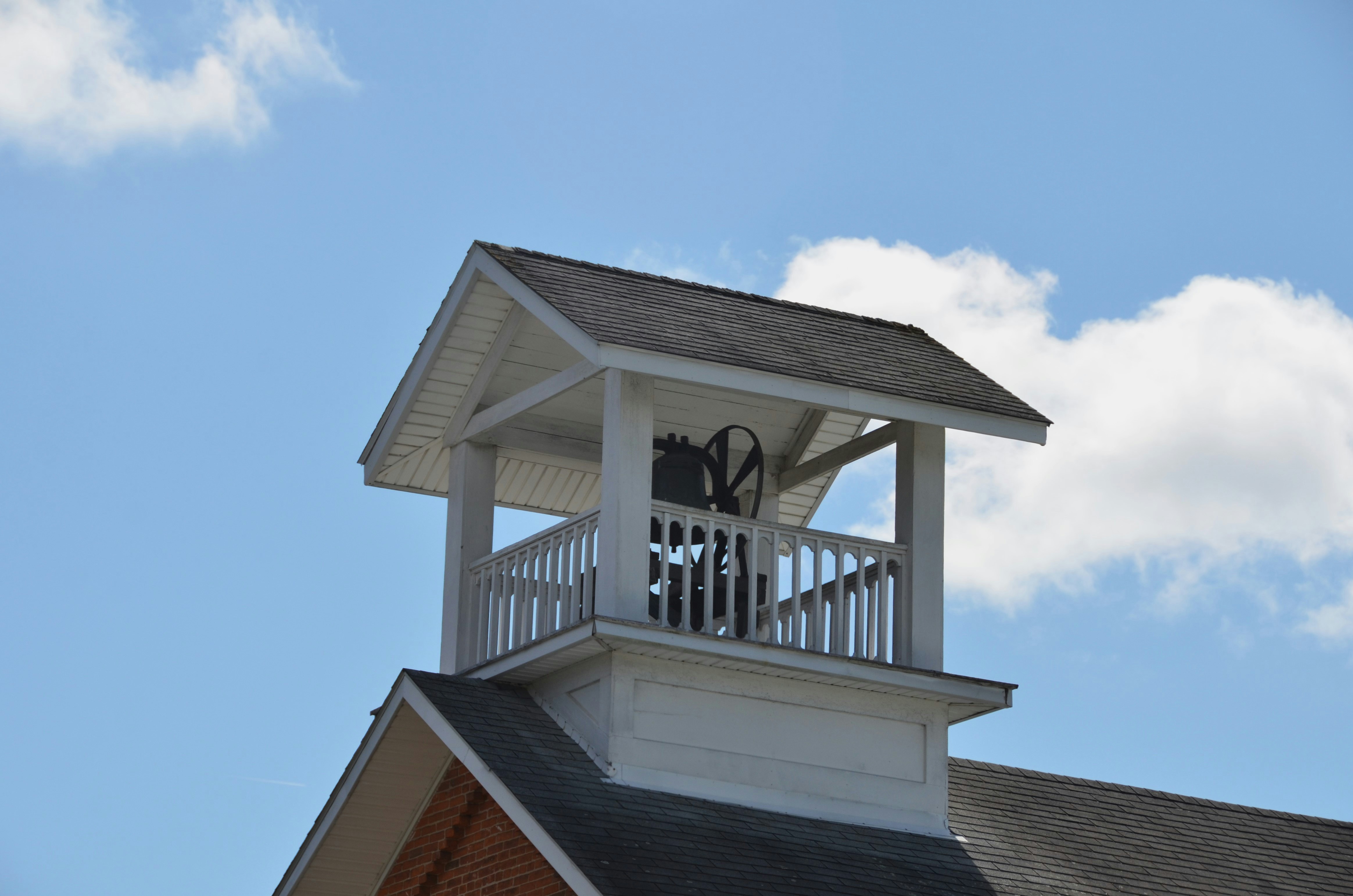 Church bell tower with wooden railing set against a bright blue sky and scattered clouds.