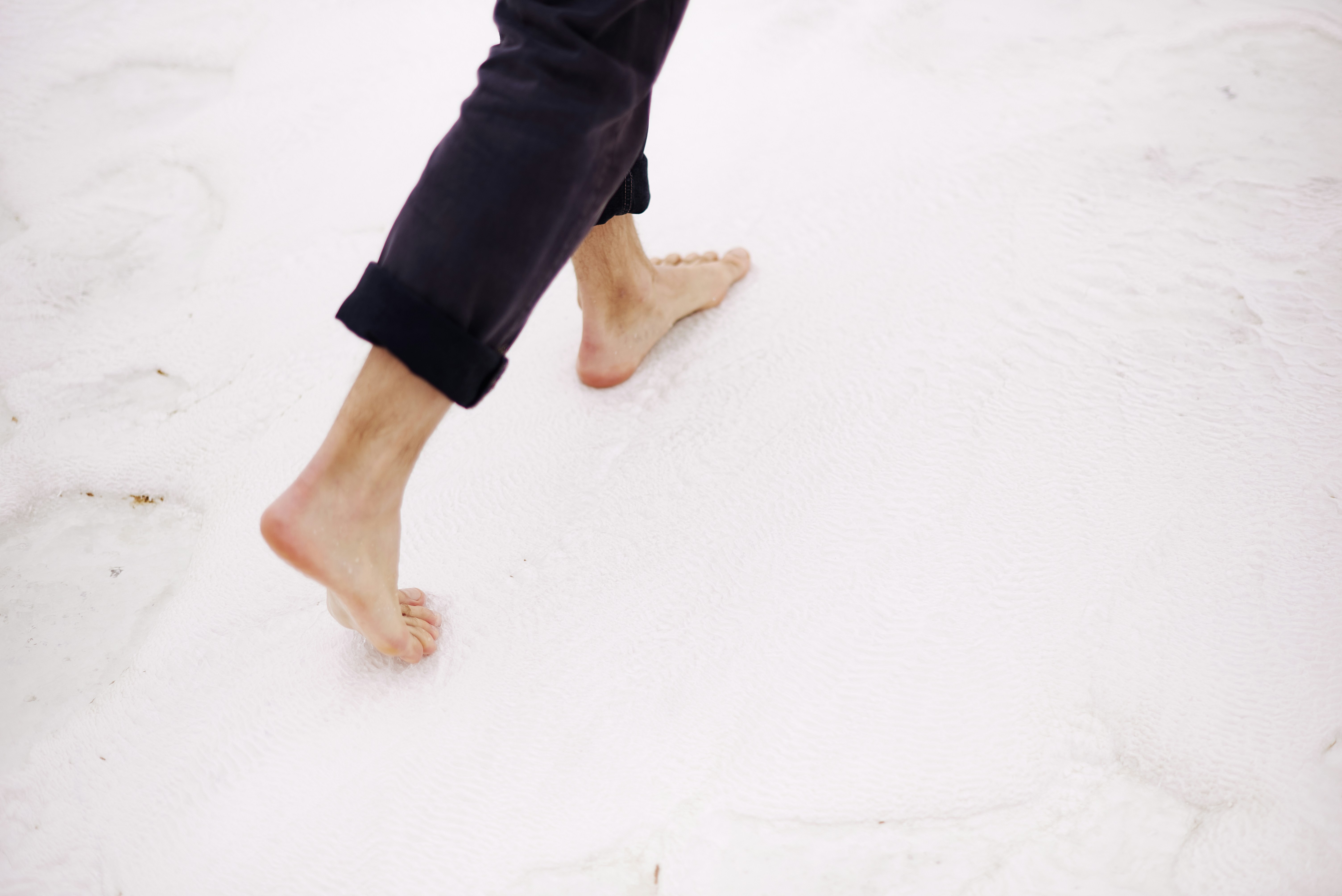 Barefoot steps leaving gentle impressions on a pristine white sandy surface.