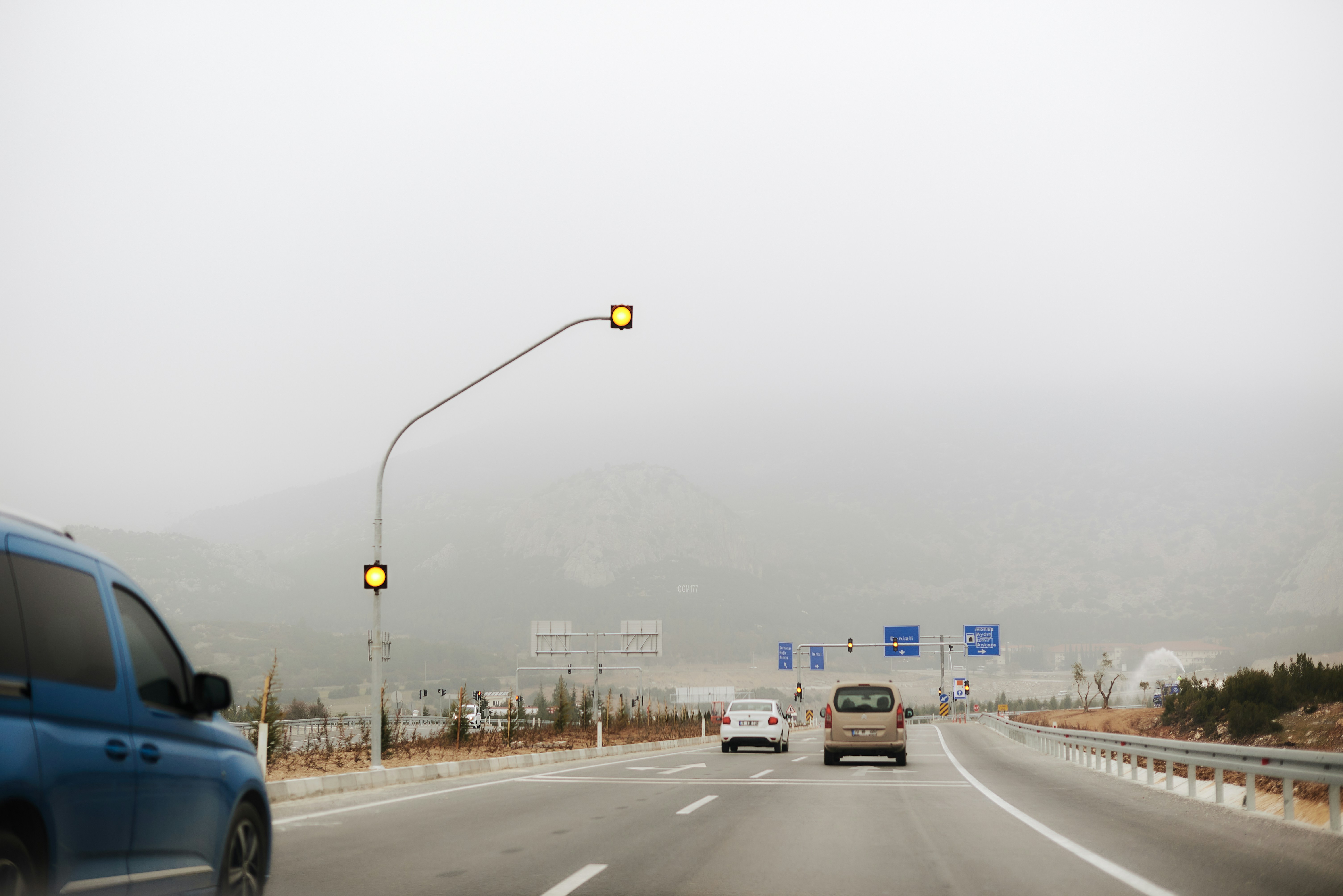 Cars travel on a foggy highway under an overcast sky with distant mountains.