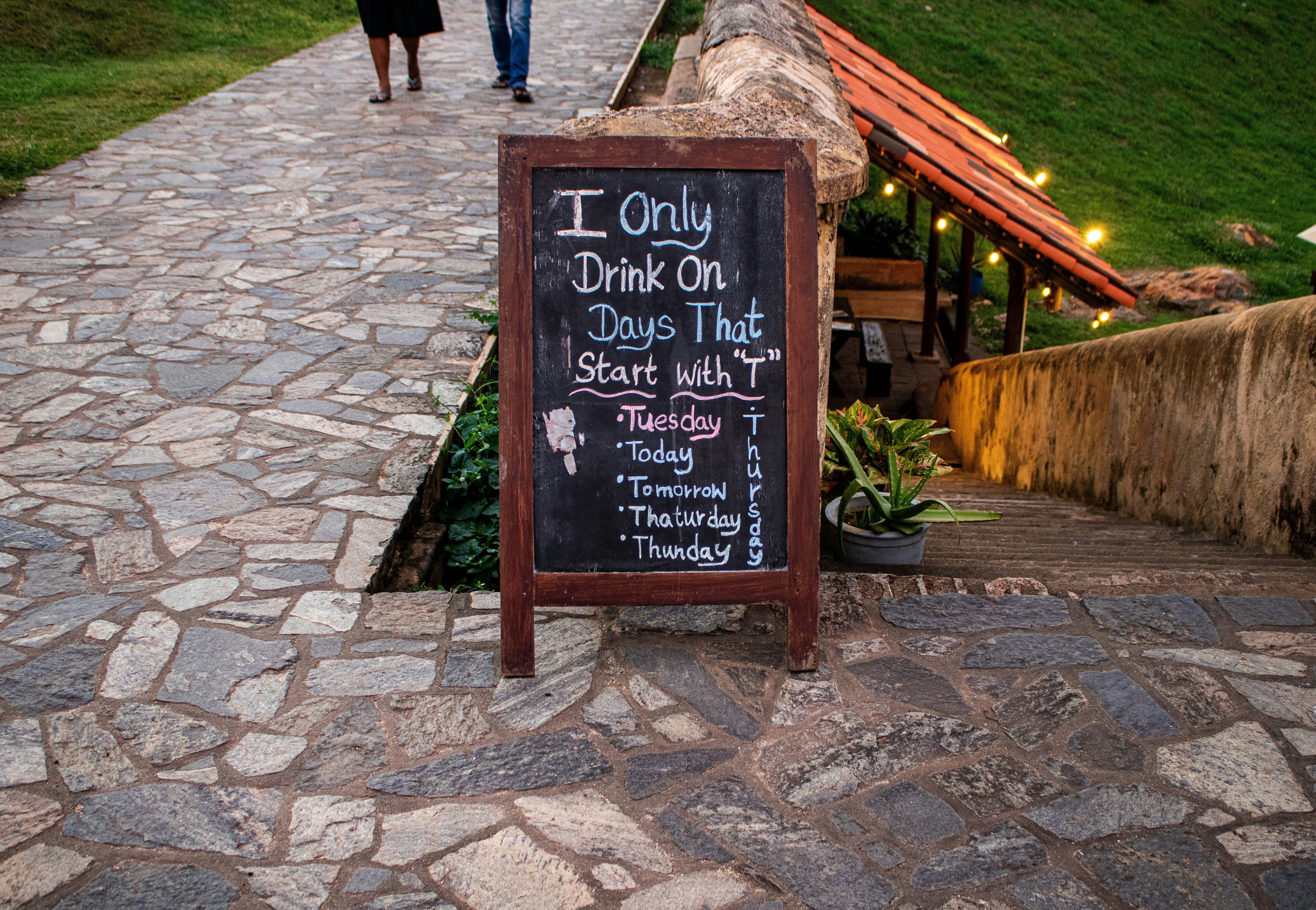 Wooden A-frame chalkboard sign with a witty message in colorful chalk on a stone-paved walkway.