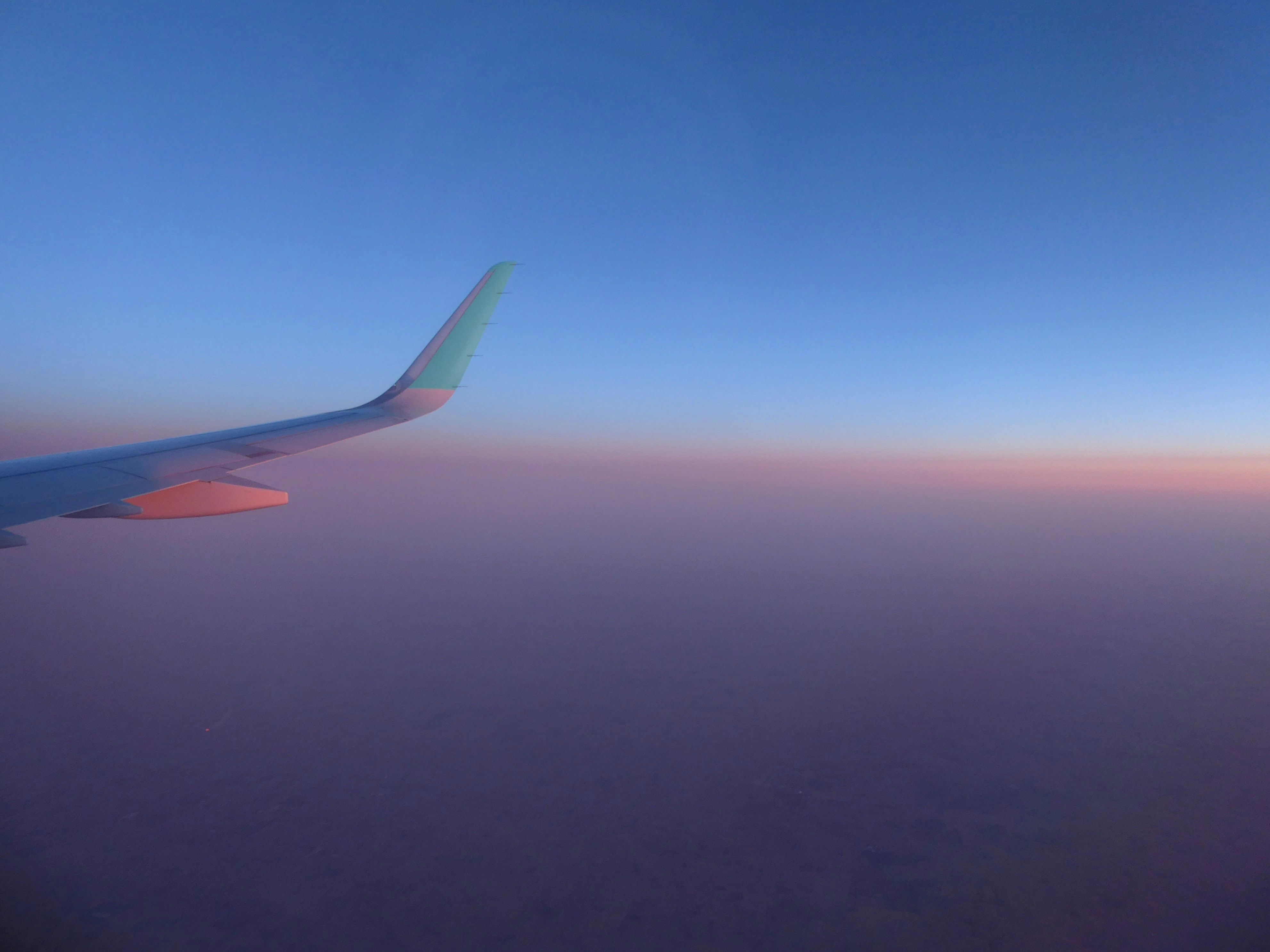Airplane wing extending into a gradient sky at dusk, blending hues of blue and purple. 