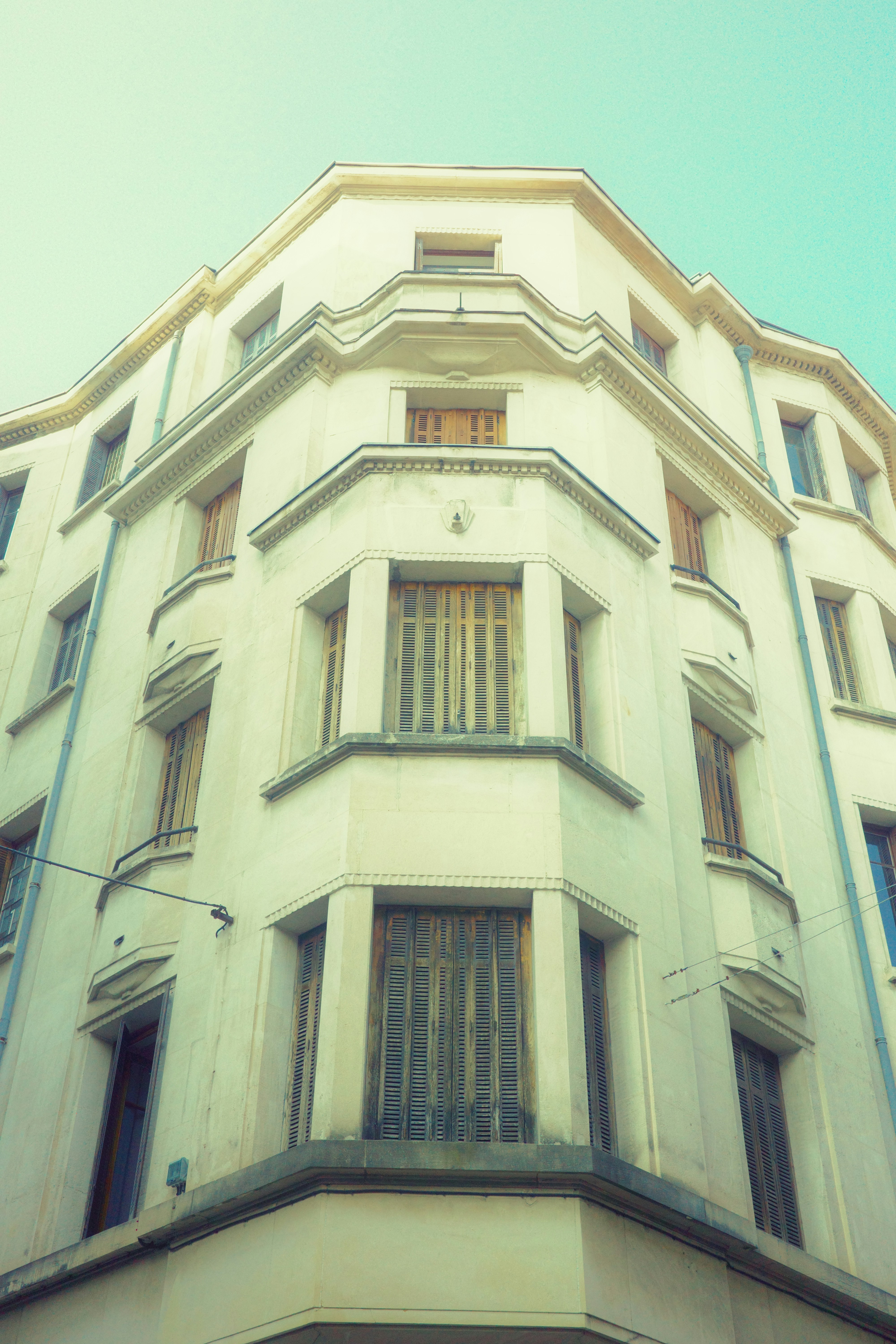 Upward view of a multi-story building with symmetrical windows and soft sunlight.