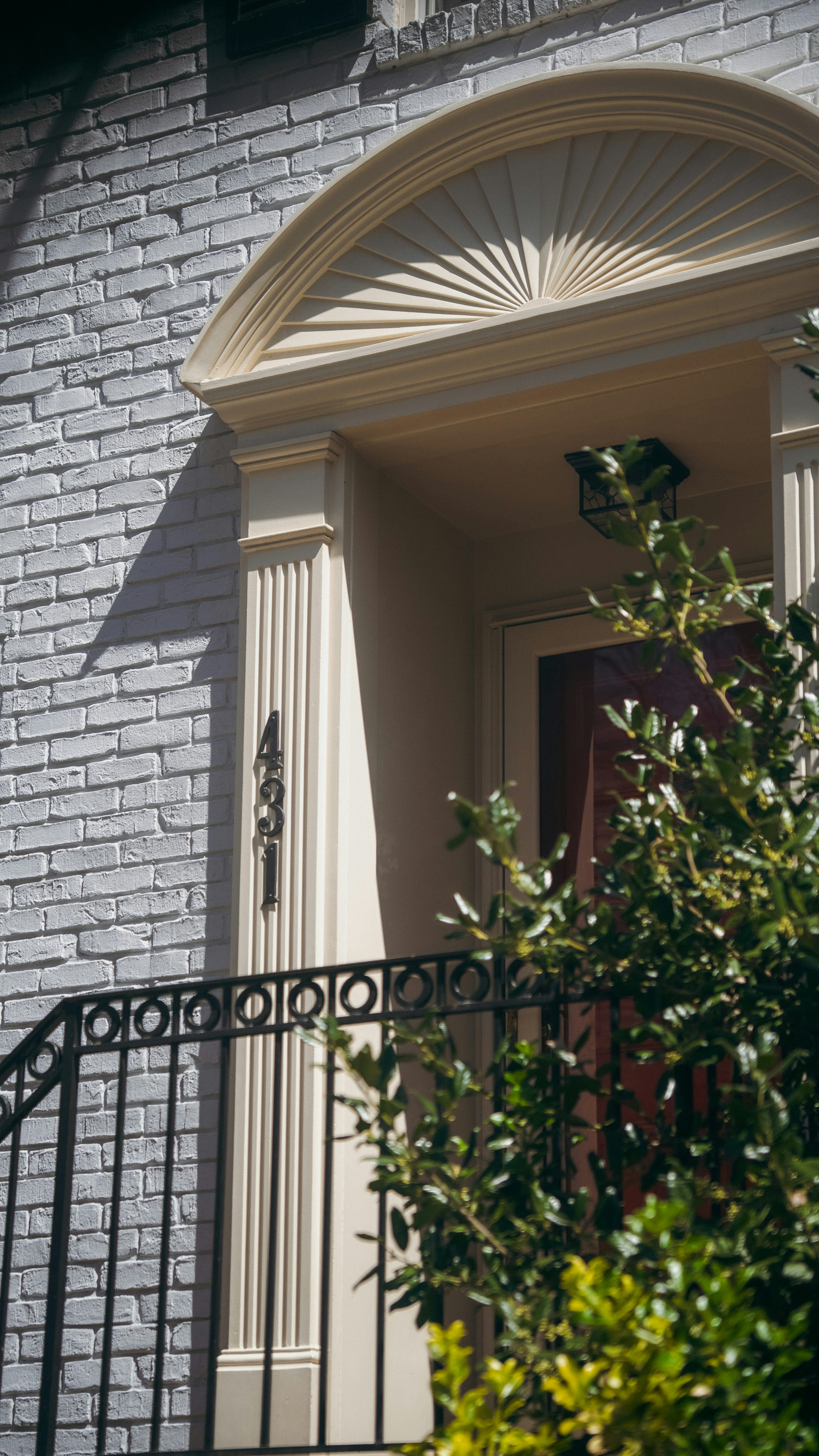 Arched entryway with ornate columns and a red door framed by leafy foliage.