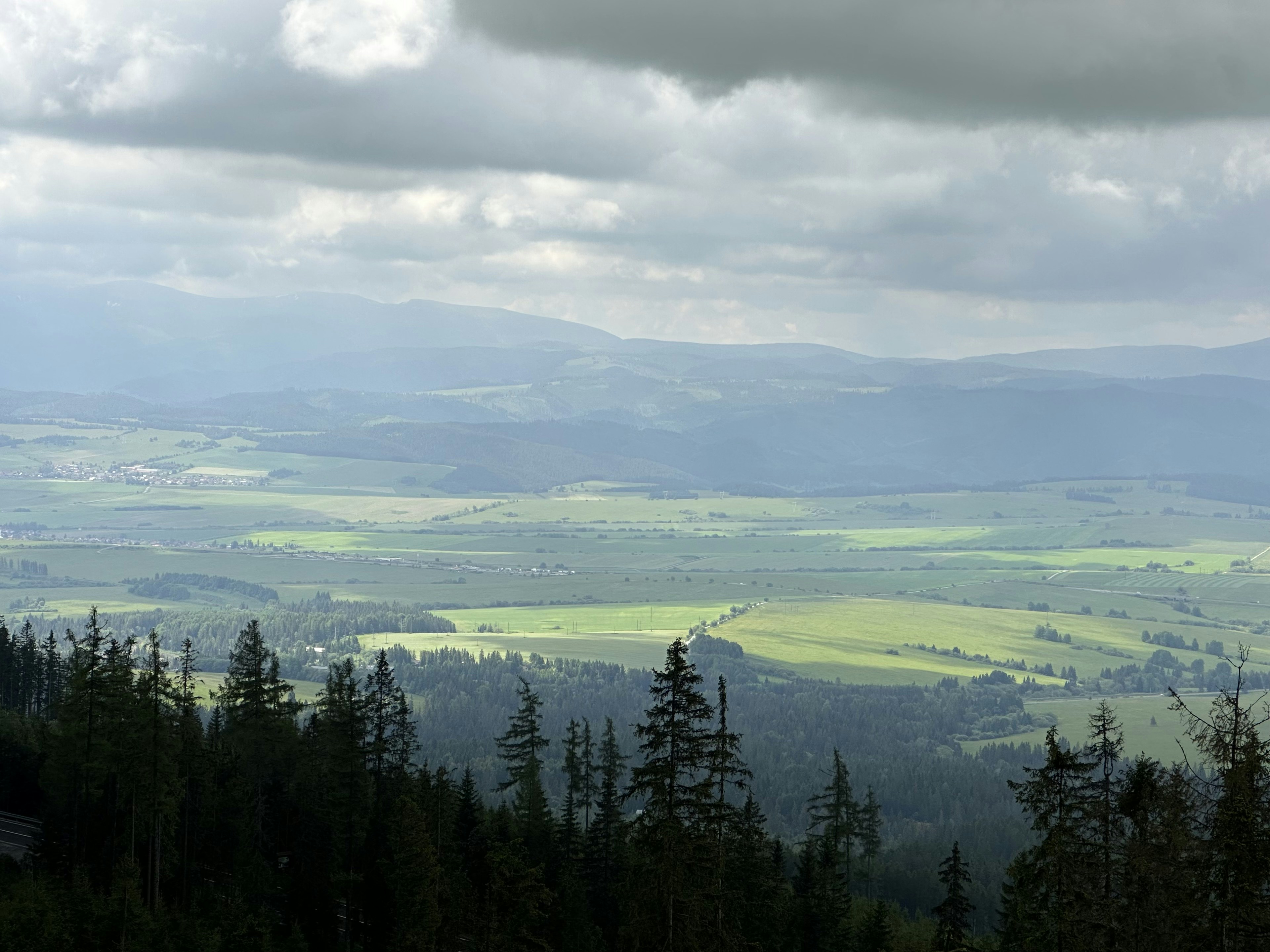 Expansive view of Poprad valley and distant Low Tatras under a cloudy High Tatras sky.