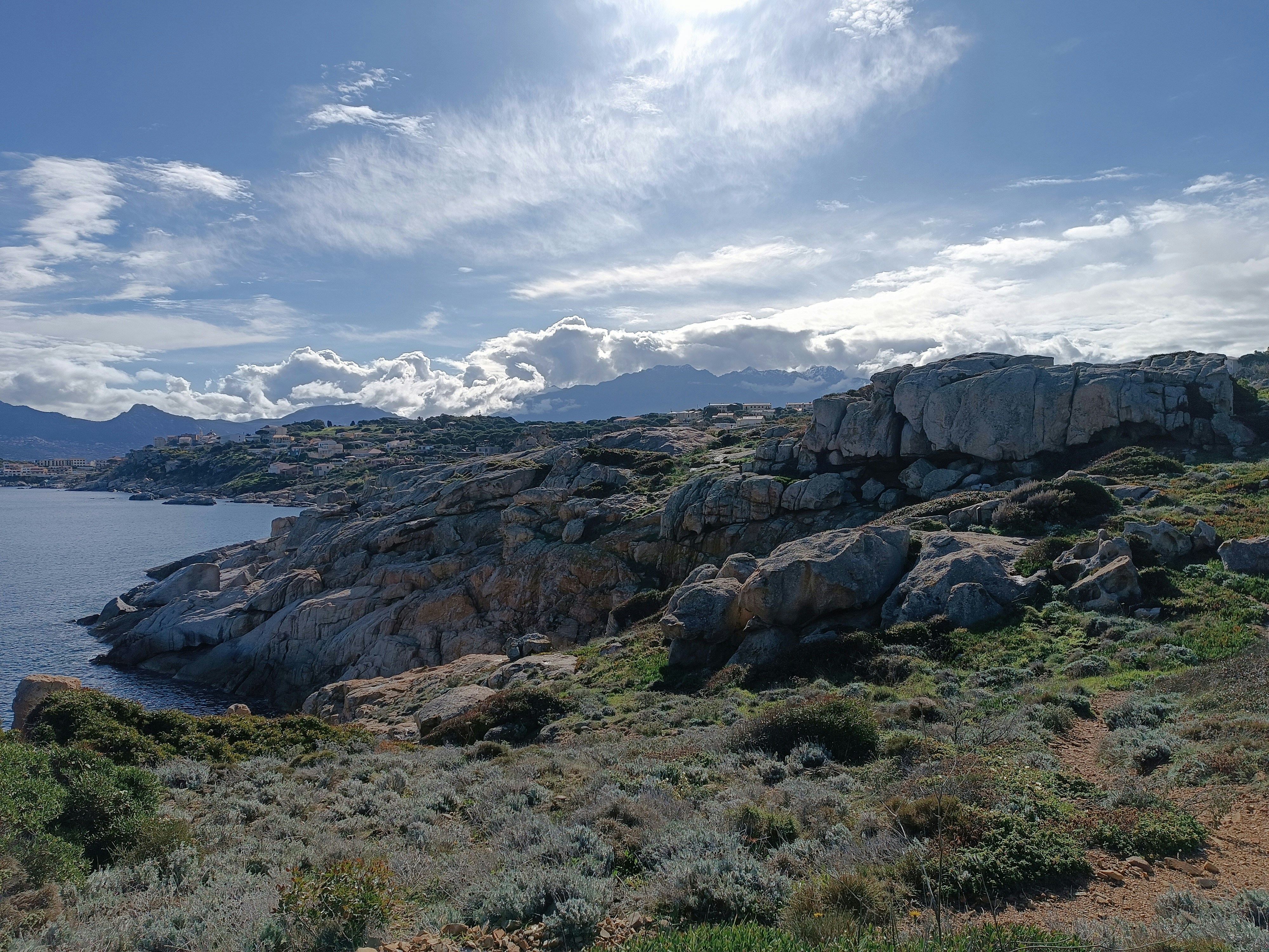 Rocky coastline under a vibrant sky with scattered clouds, showcasing the natural beauty of the terrain. The scene highlights the interplay between land and sea.