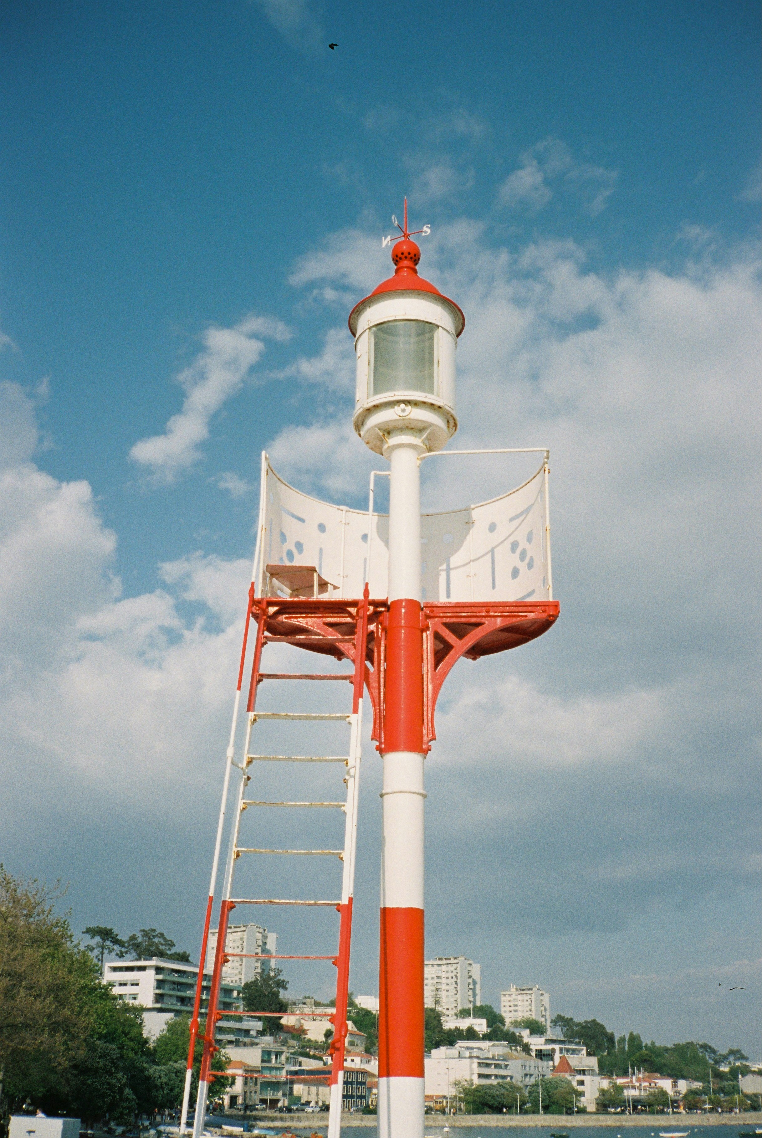 Beacon in a Breeze: Red-White Lighthouse Over a Quiet Seaside Quarter