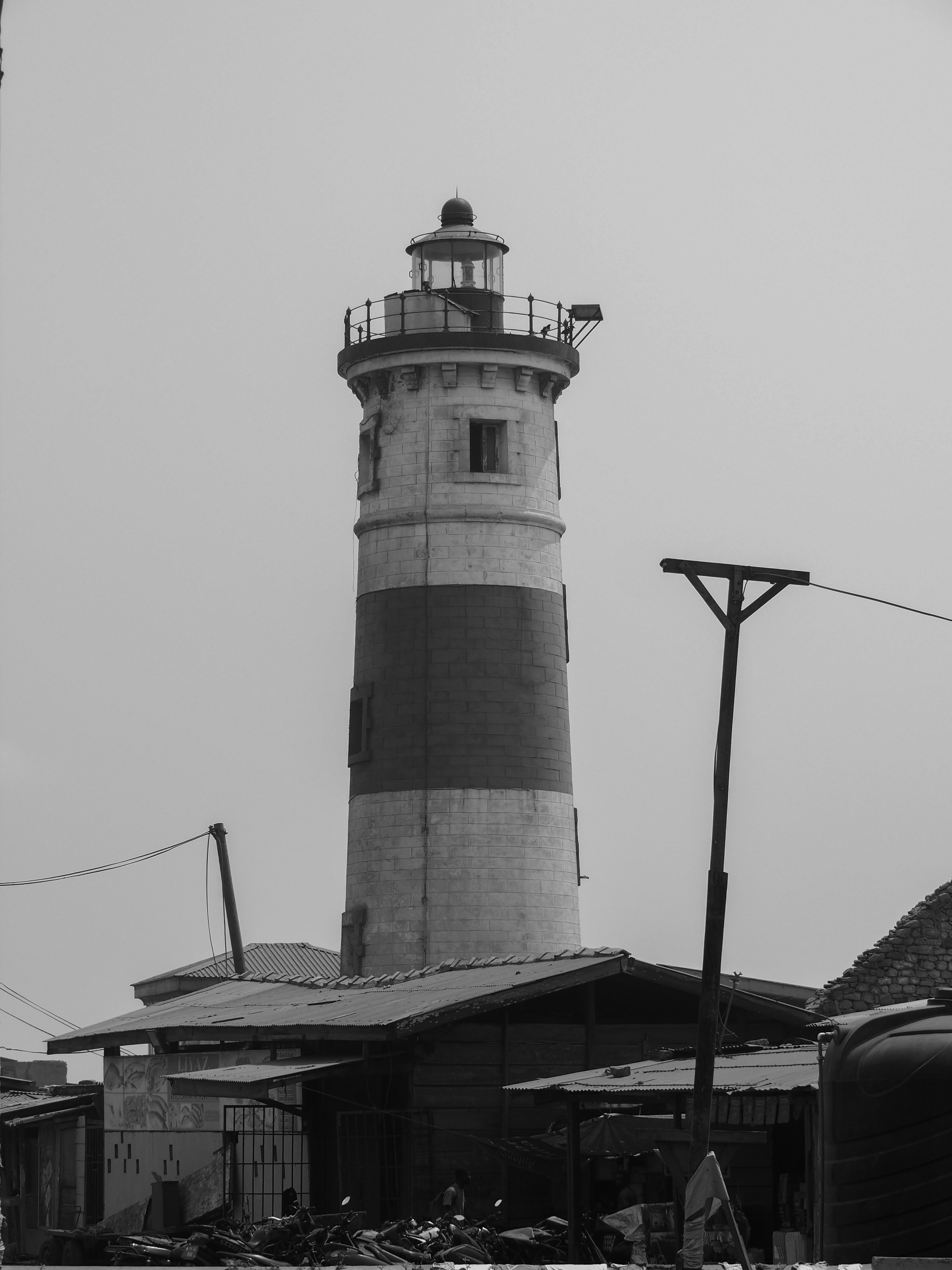 Monochrome Beacon Amid Industrial Quiet: A Lighthouse Atop a Weathered Shoreline
