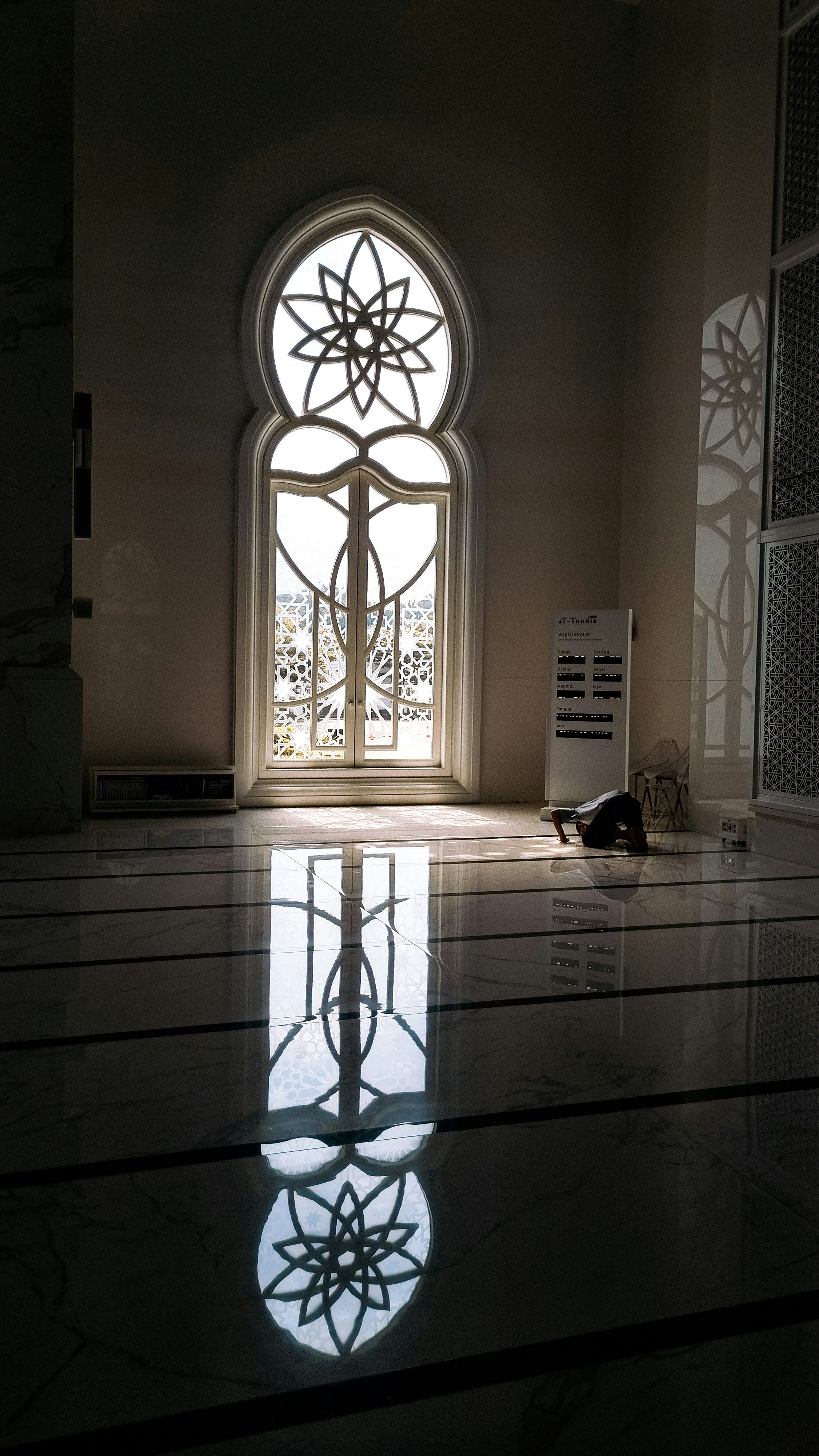 Ornate window casting intricate shadows and reflections on a polished floor in a dimly lit room.