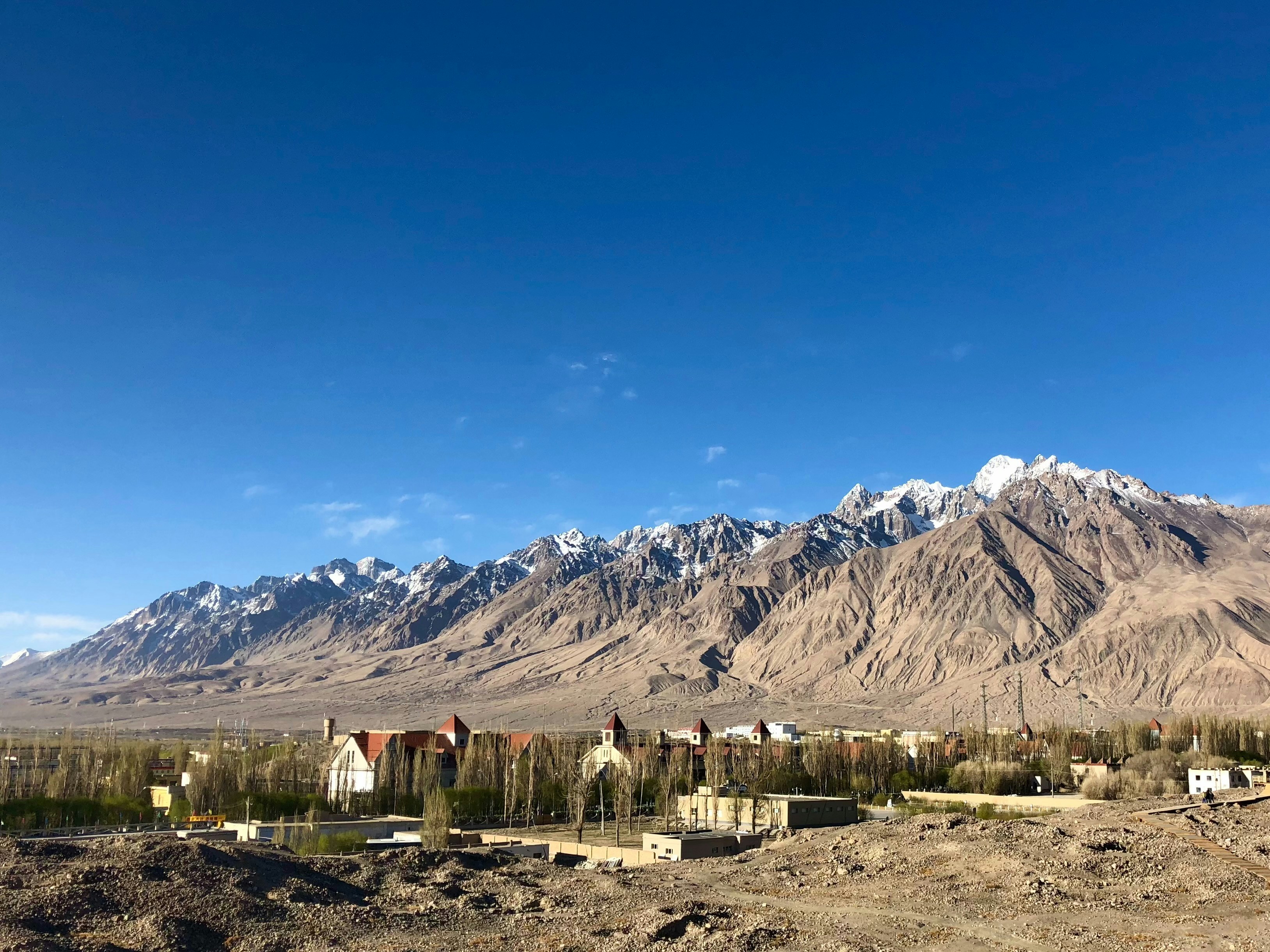 Snow-capped mountains rise behind a small settlement under a clear blue sky.