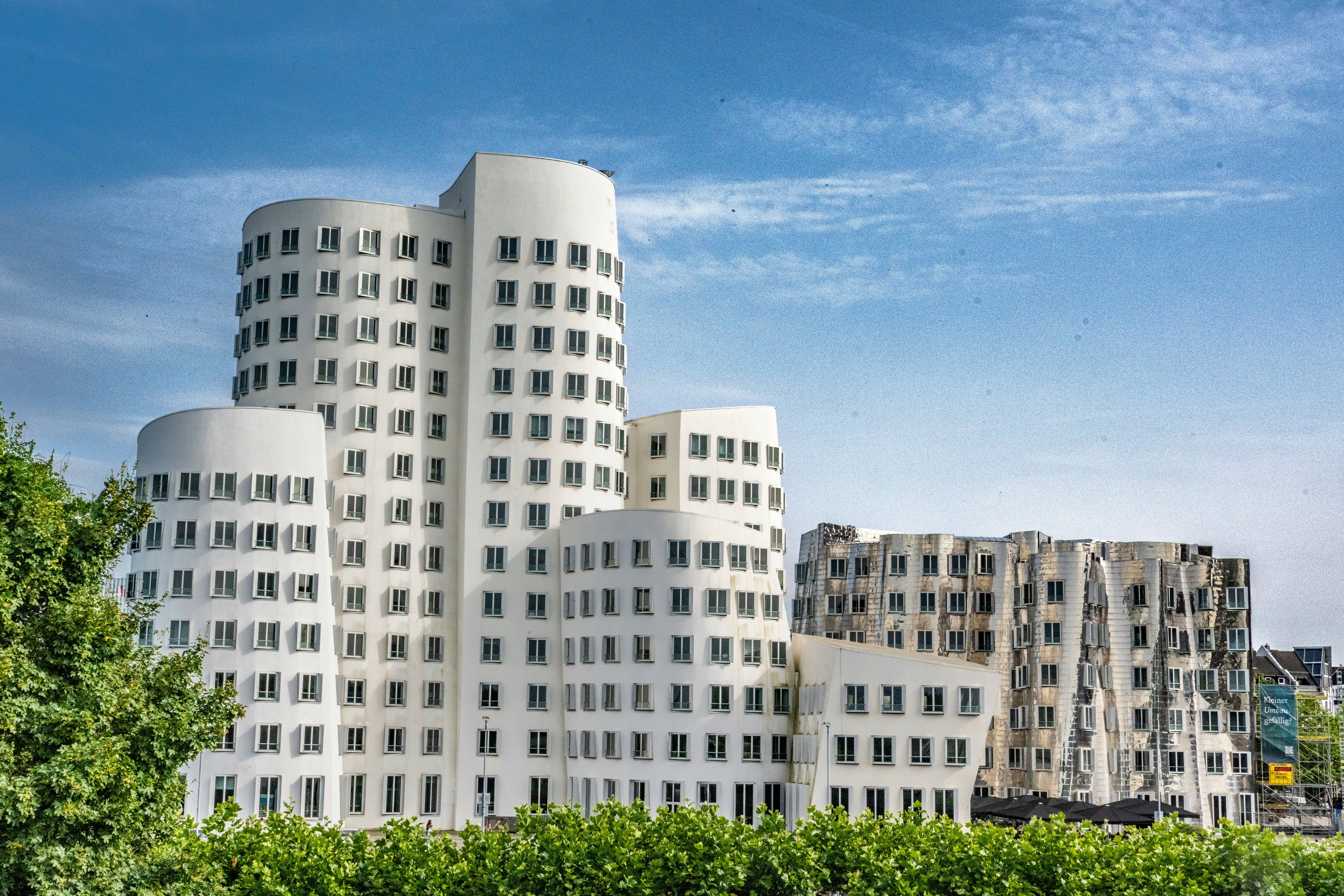 Modern white and metallic buildings with curved surfaces under a clear blue sky.
