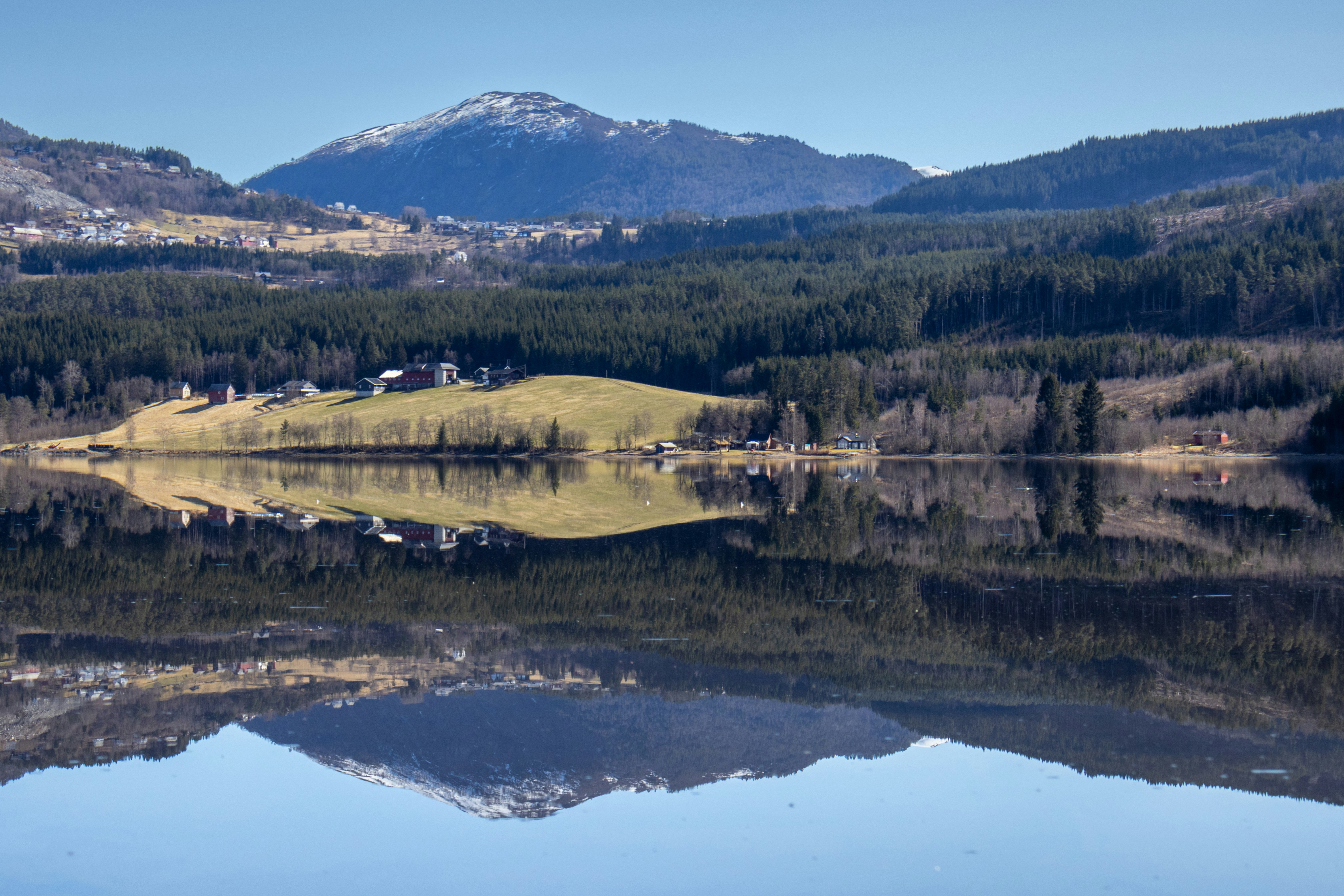 Tranquil lake reflecting a mountainous landscape under a clear blue sky.