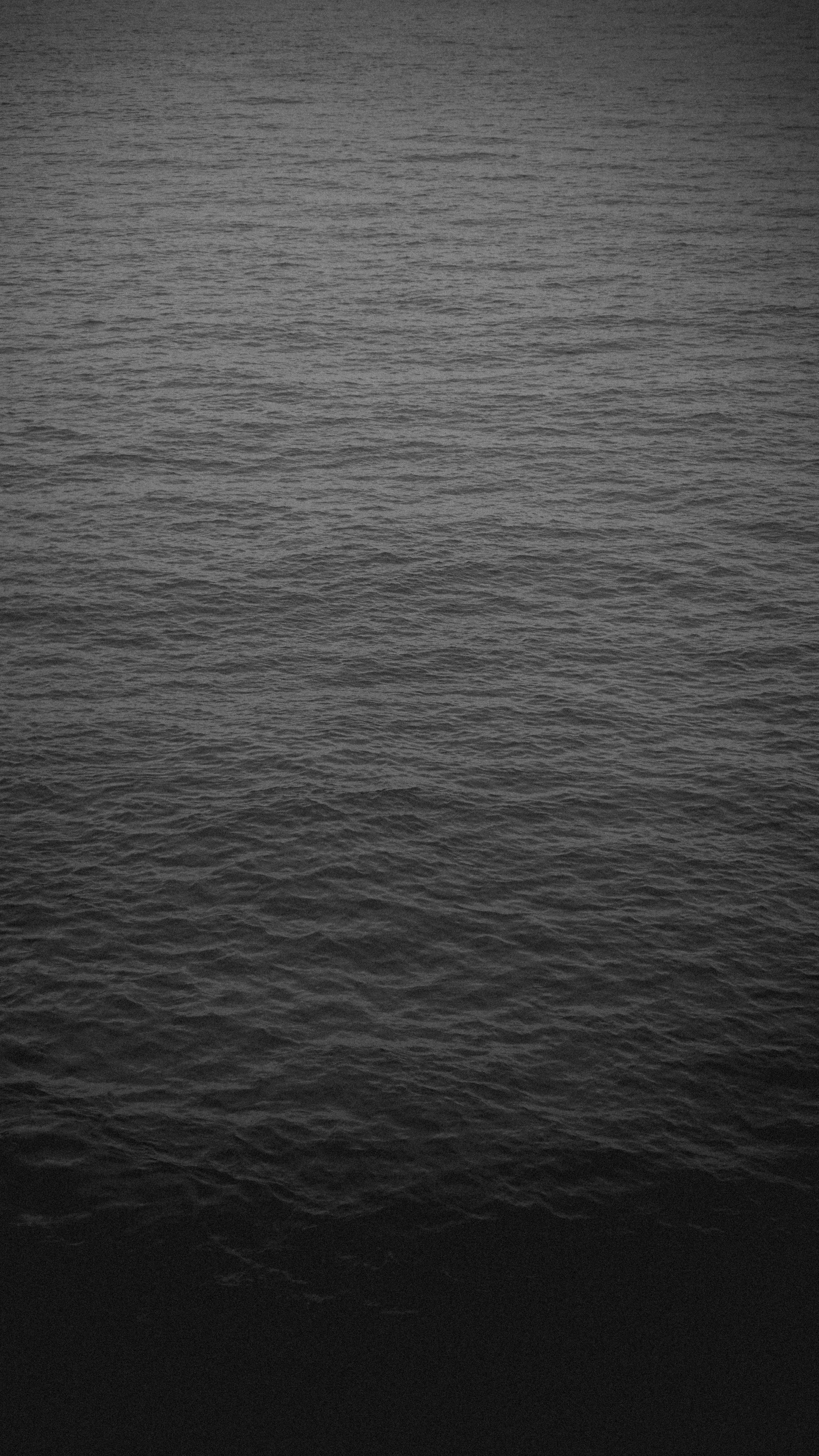 Gentle ripples on a dark, monochromatic sea surface.
